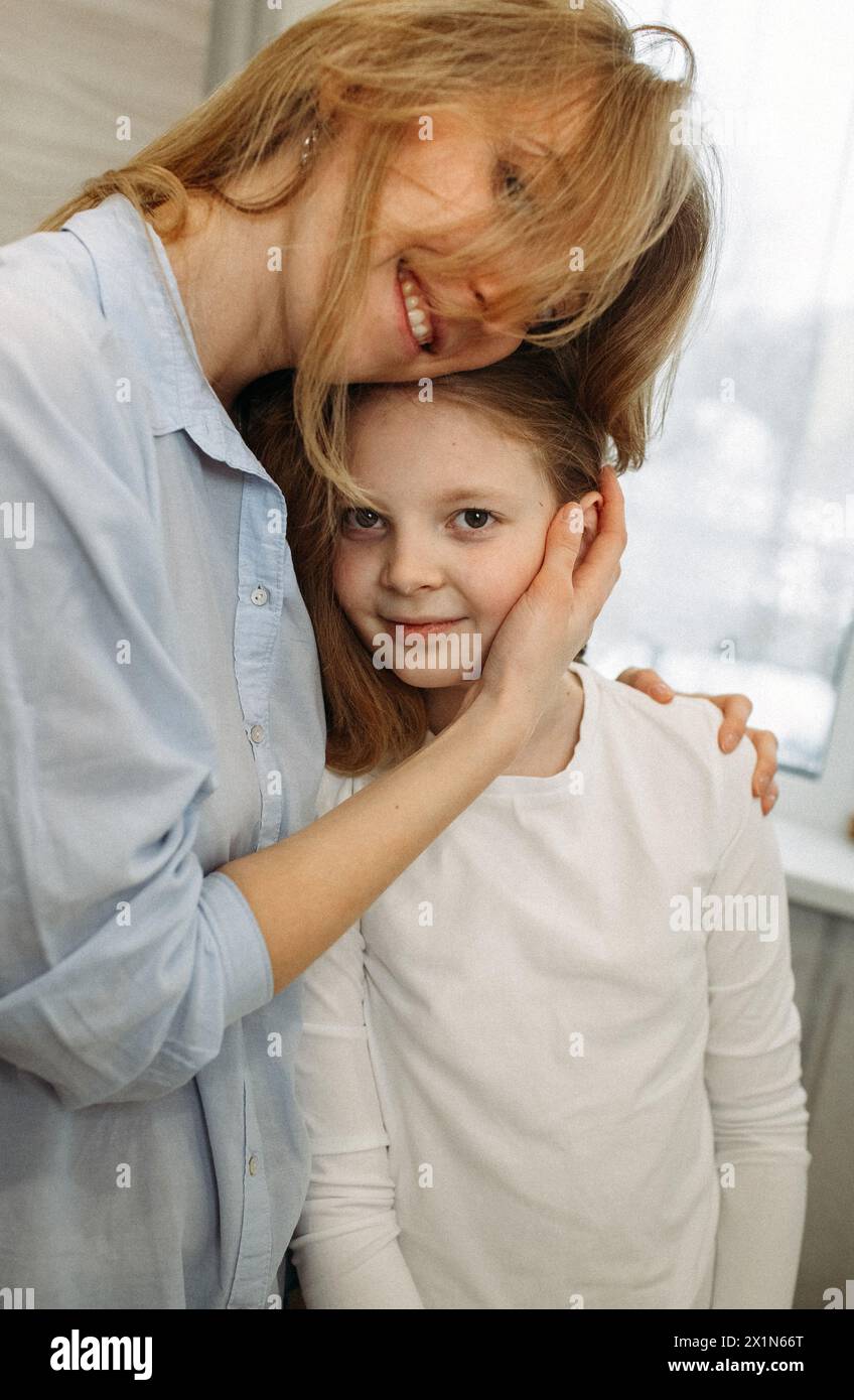 A woman is embracing a young girl in a warm hug in the kitchen. The two ...
