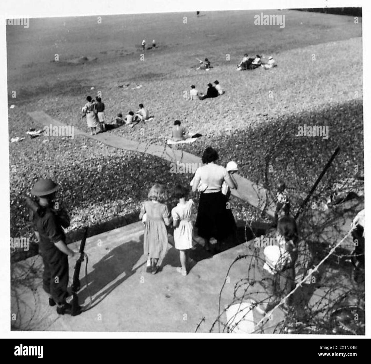 A sentry stands on duty observing groups enjoying a day at the seaside ...