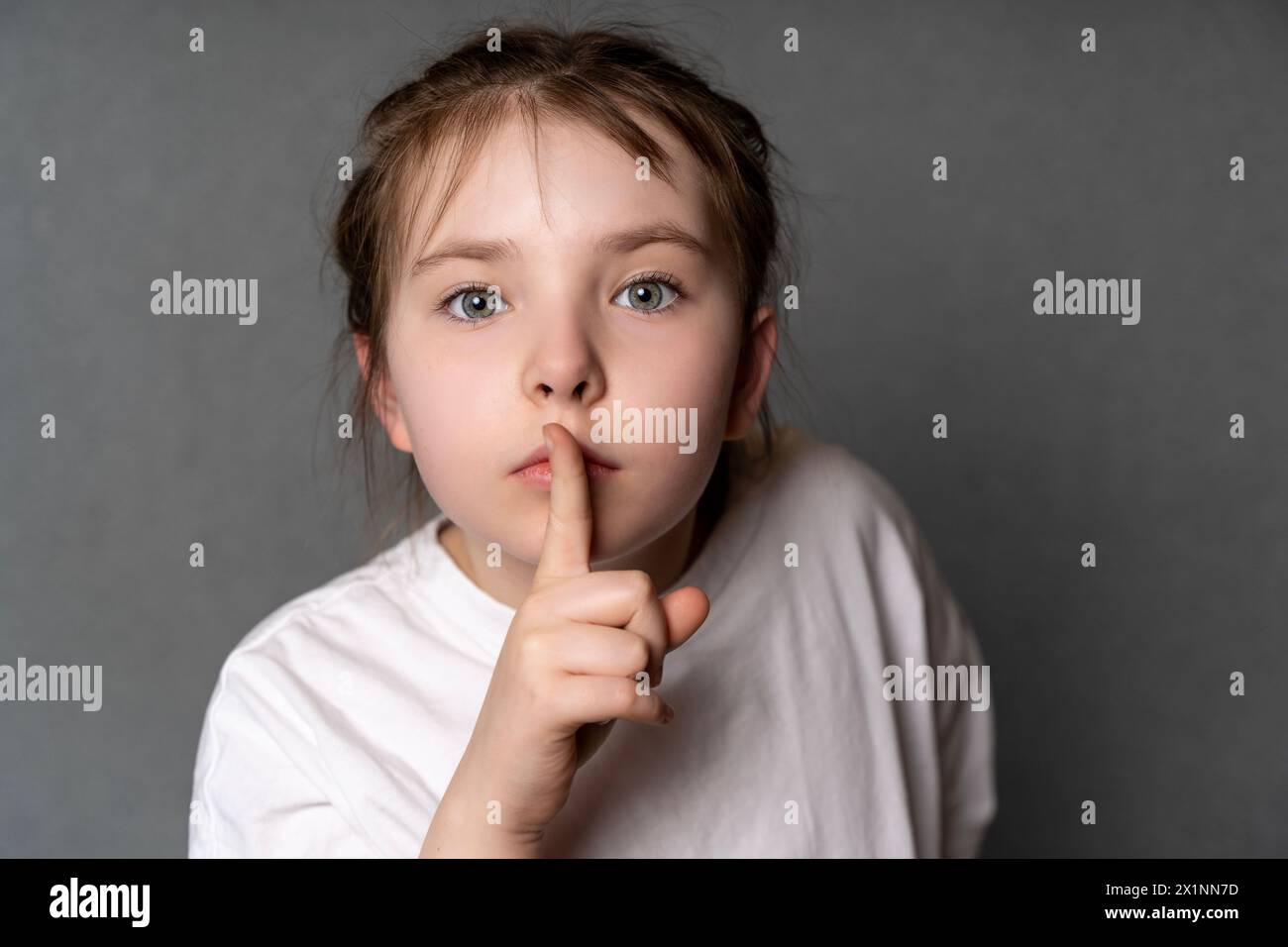 Portrait of a little cute teenage girl showing a sign of silence with a ...