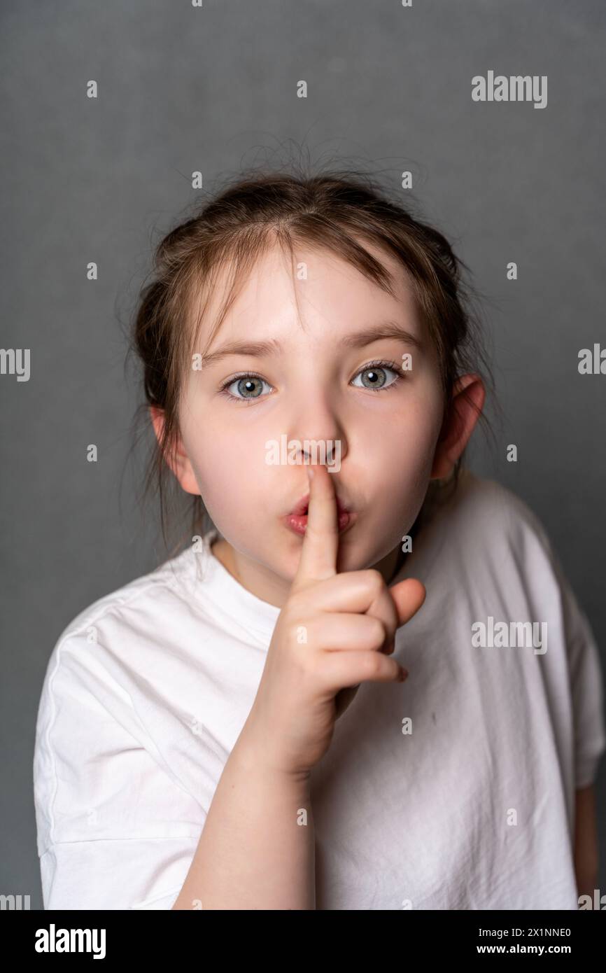 Little teenage girl holding her finger to her mouth showing a sign of ...