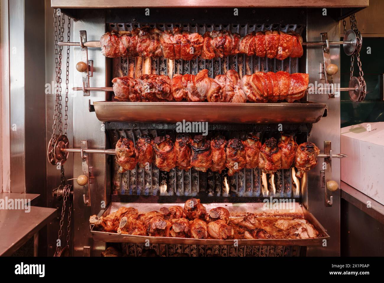 An industrial rotisserie grill oven with multiple skewers of golden ...