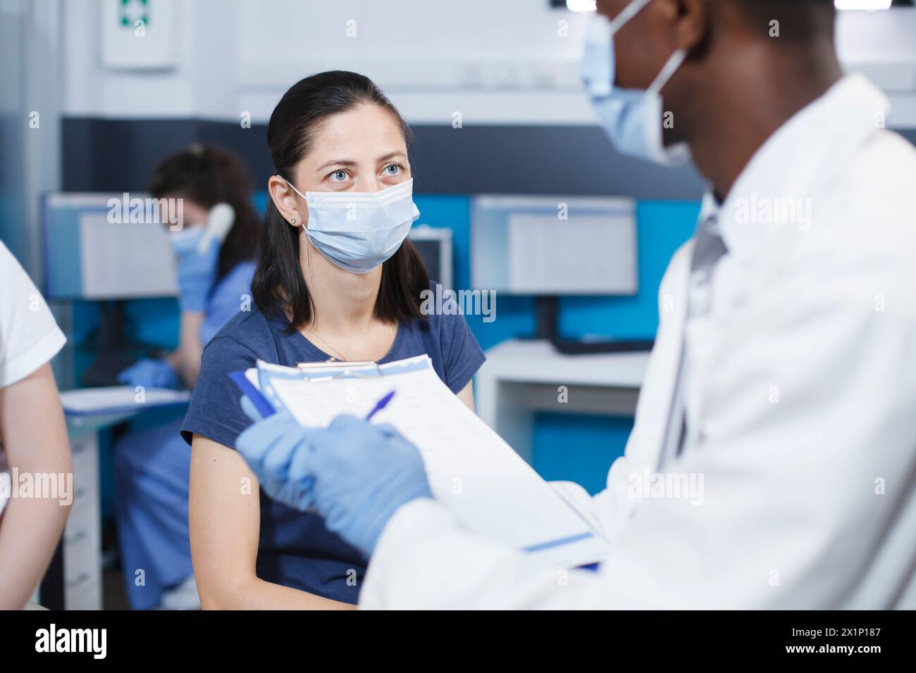 Close-up of a doctor in a lab coat and face mask talking to a caucasian ...