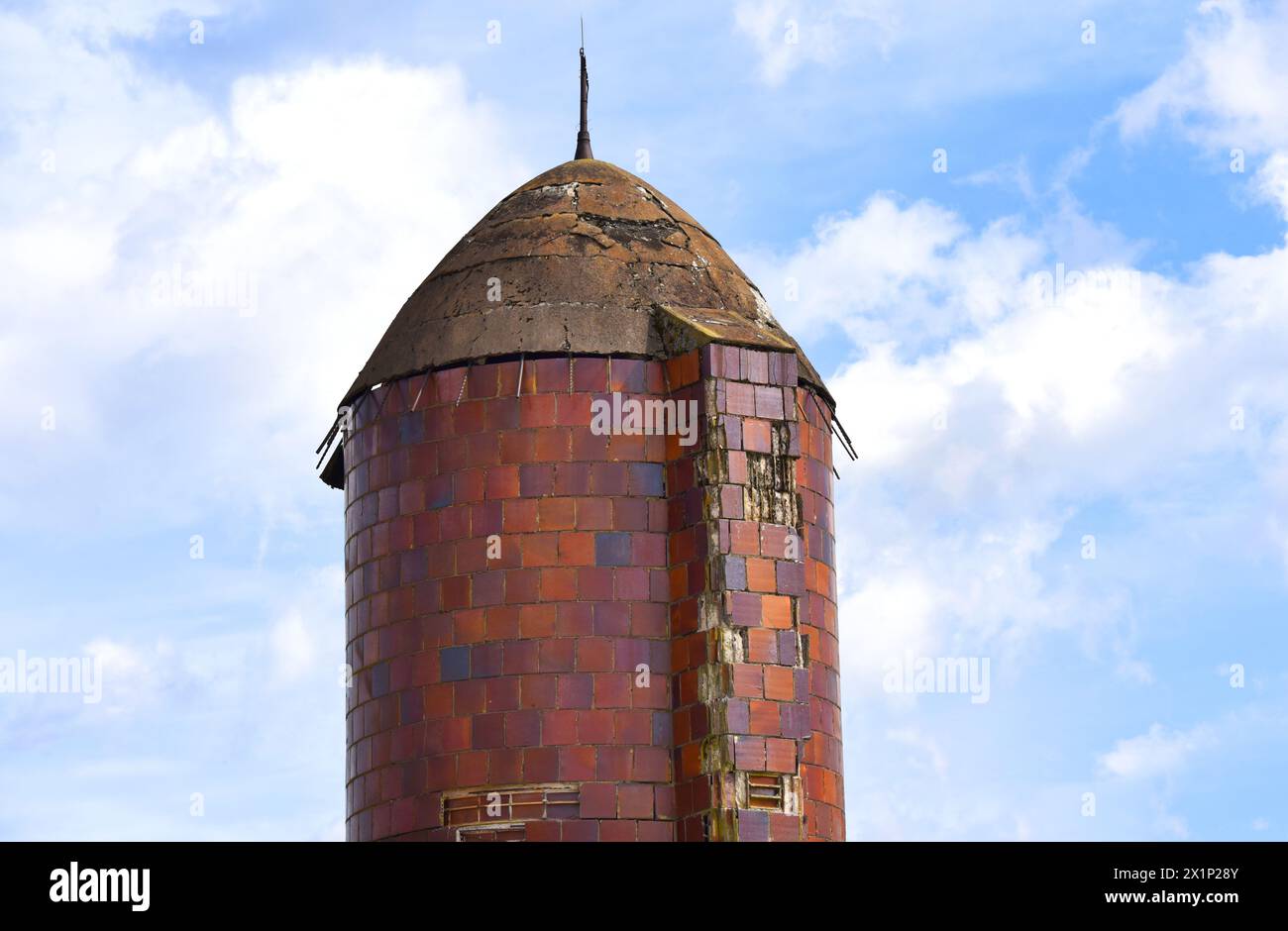 Old silo is constructed of red tiles. Top is brown shingles and is ...