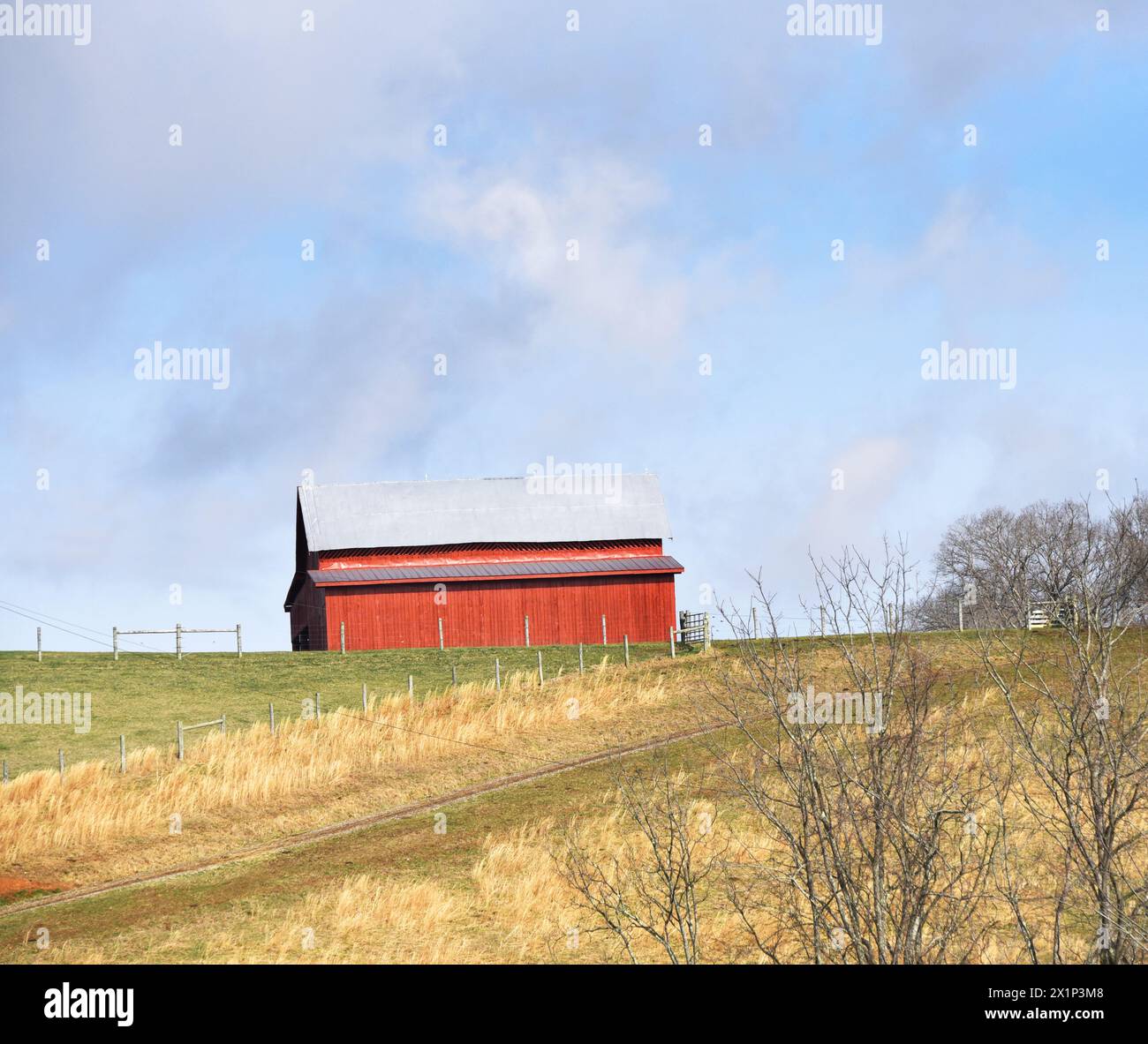 Red, wooden barn sits on the top of a hill. Dirt lane runs diagonally ...