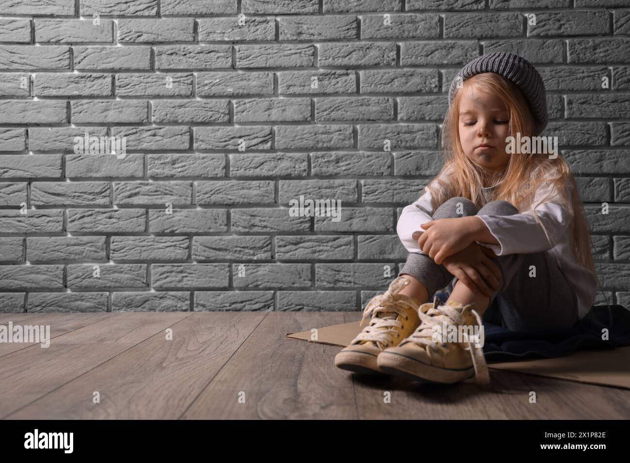 homeless little girl sitting on floor near grey brick wall Stock Photo ...