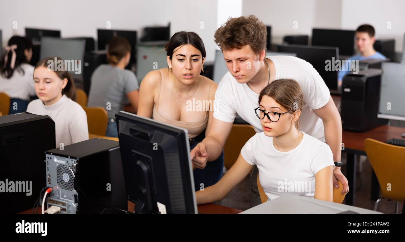 Concentrated boy helping young female students working with pc in ...