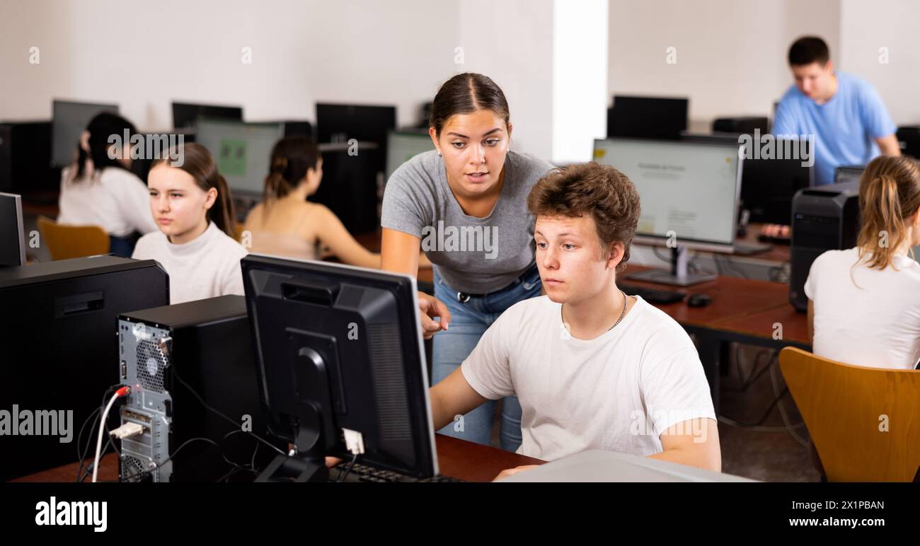 Young woman teacher helping concentrated teen male student with his ...