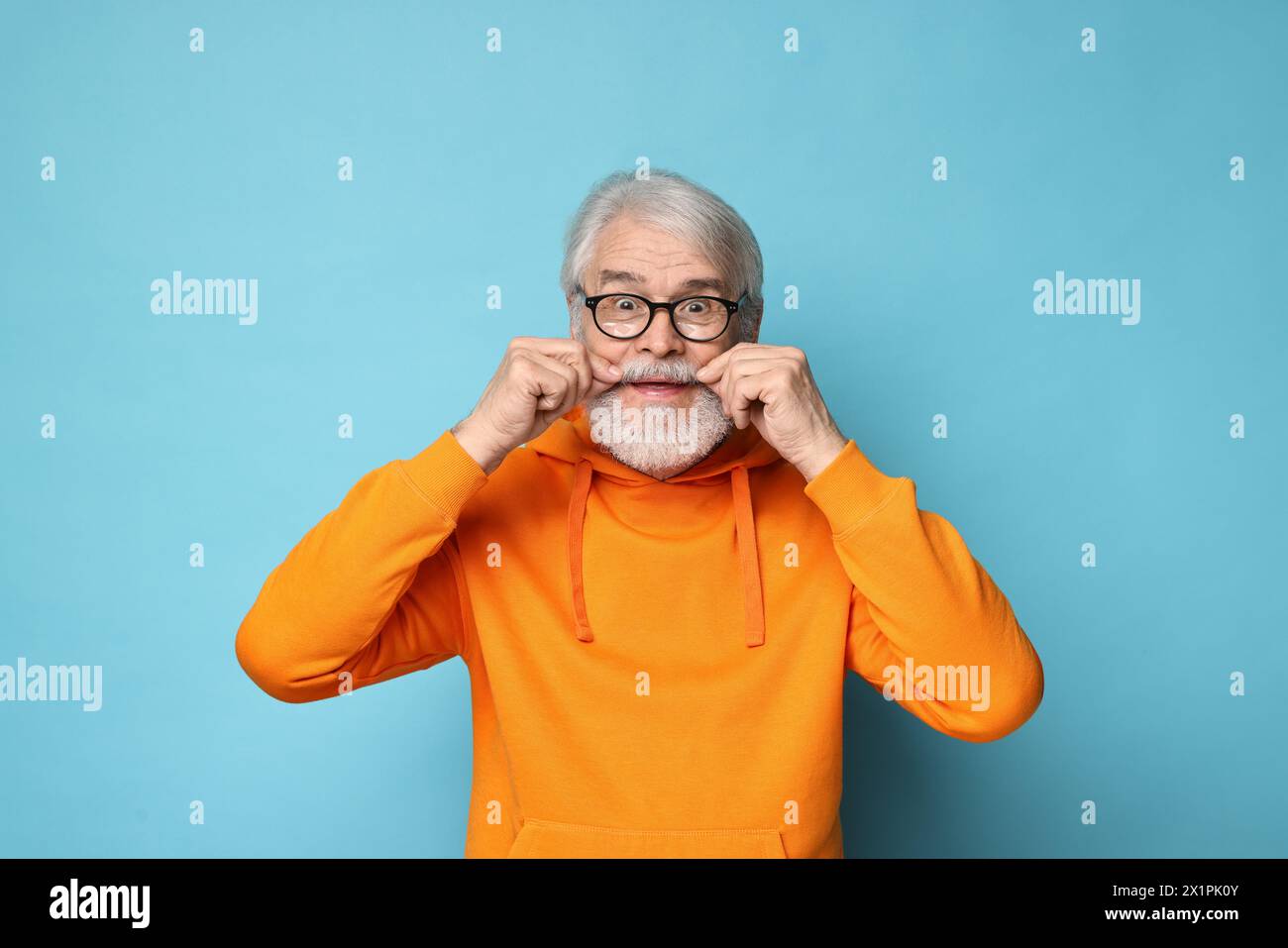 Senior man touching mustache on light blue background Stock Photo - Alamy