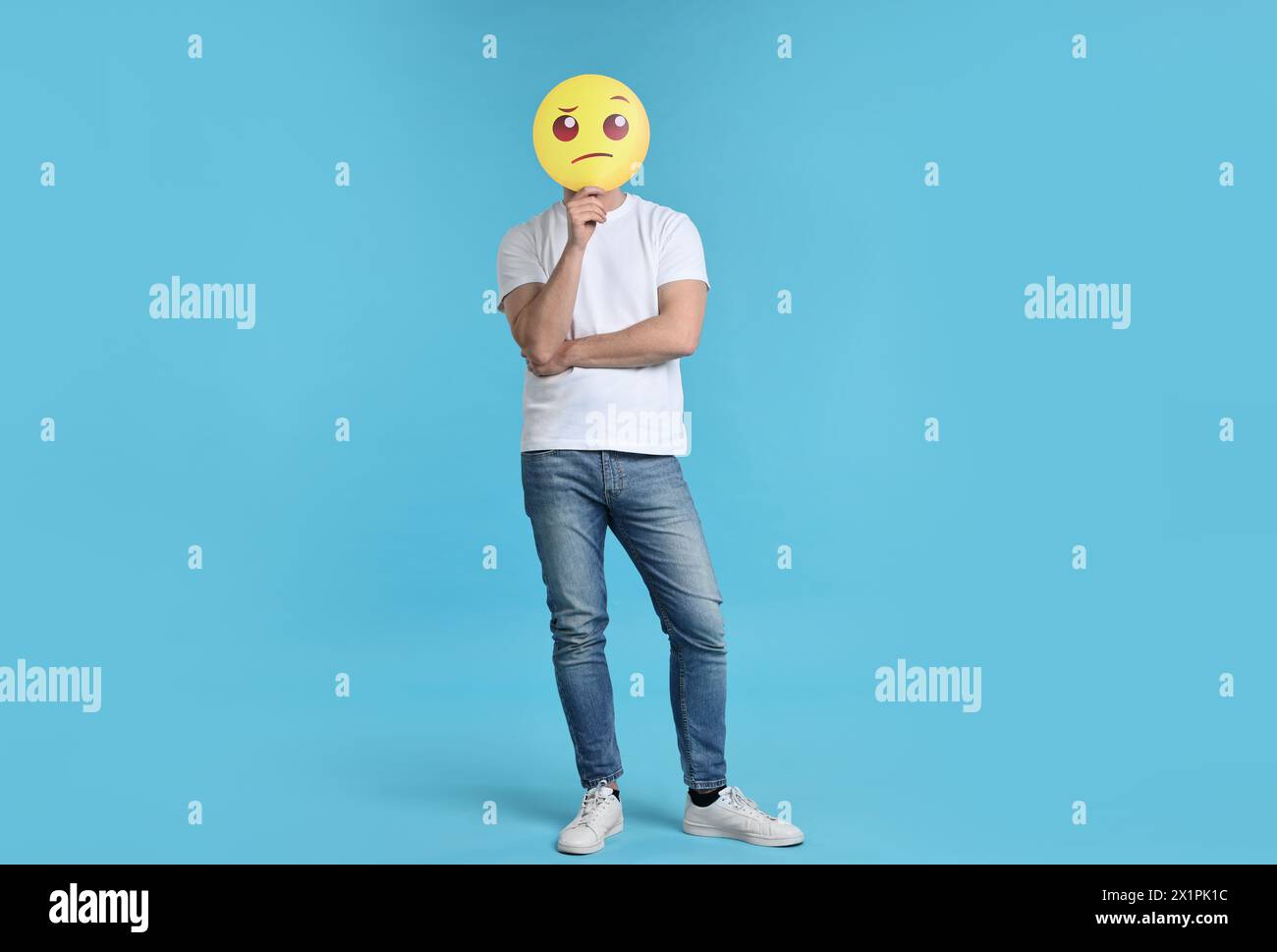 Man covering face with thinking emoticon on light blue background Stock ...