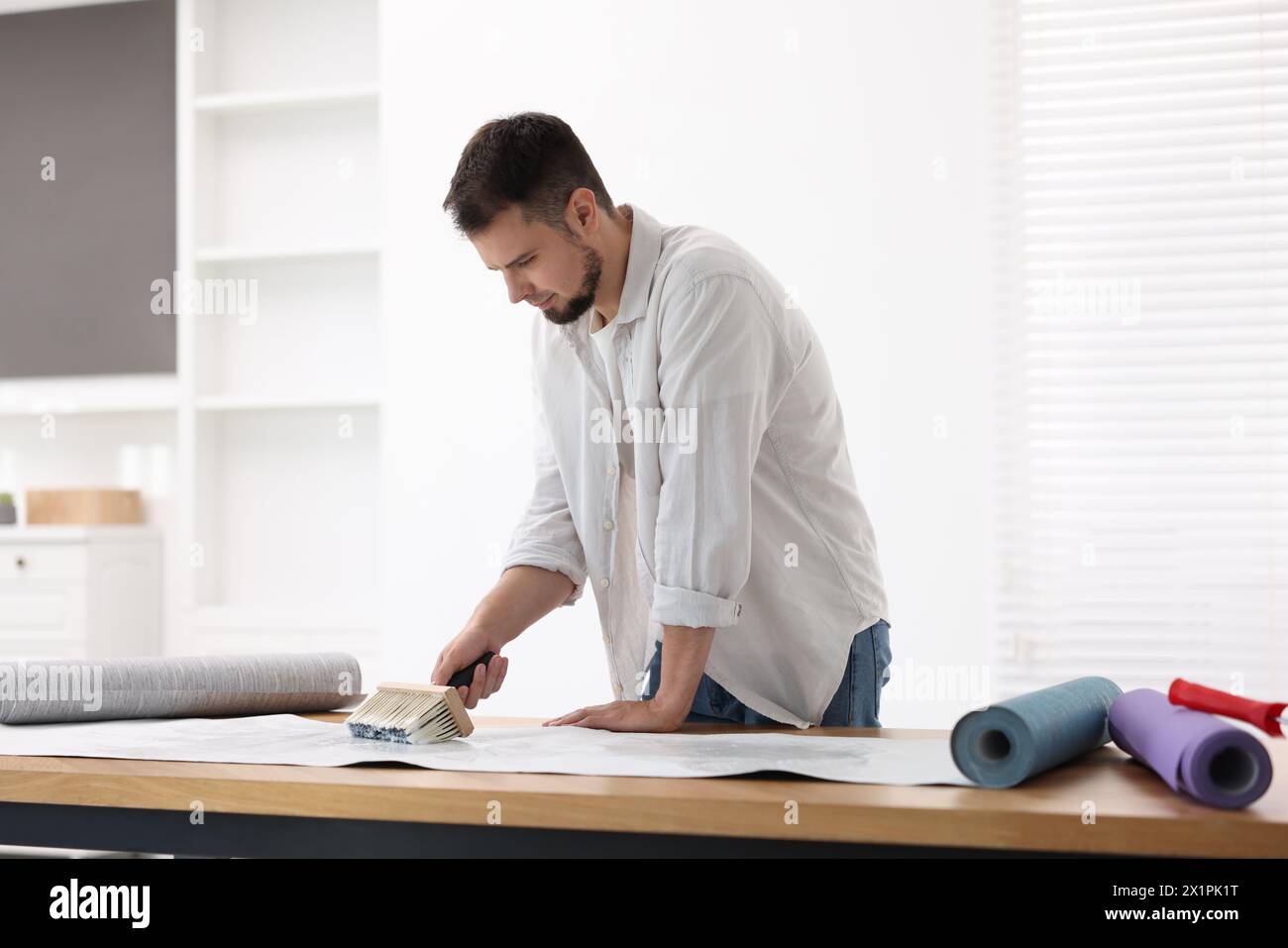 Man applying glue onto wallpaper sheet at wooden table indoors Stock ...
