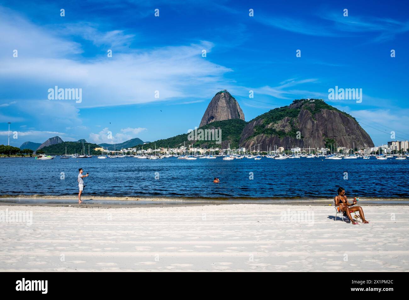 A Young Woman Reading A Book On Botafogo Beach With Sugarloaf Mountain ...