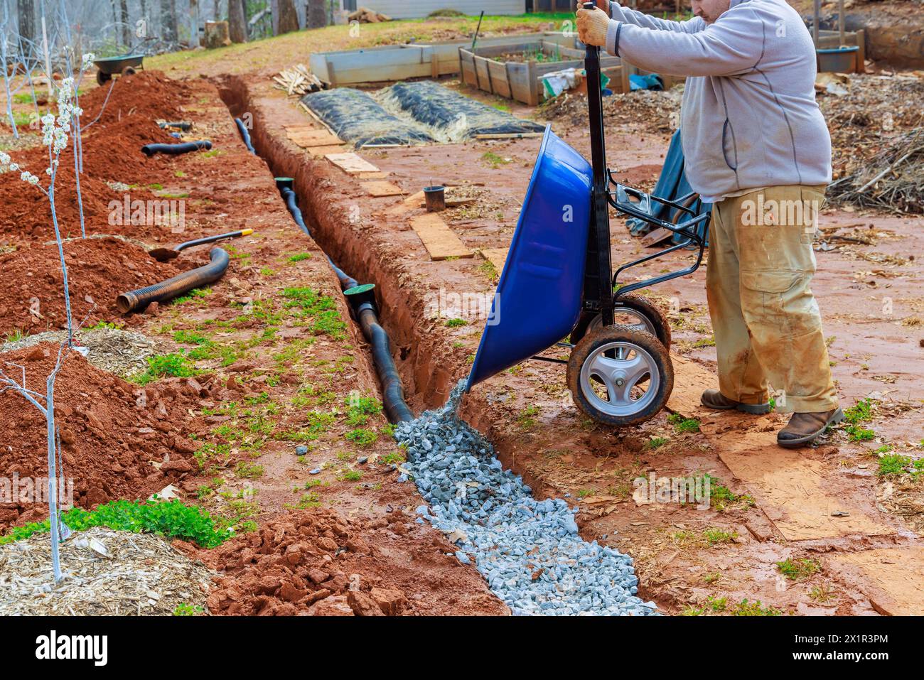 Crushed stone is fills into drainage pipes by worker using wheelbarrow ...