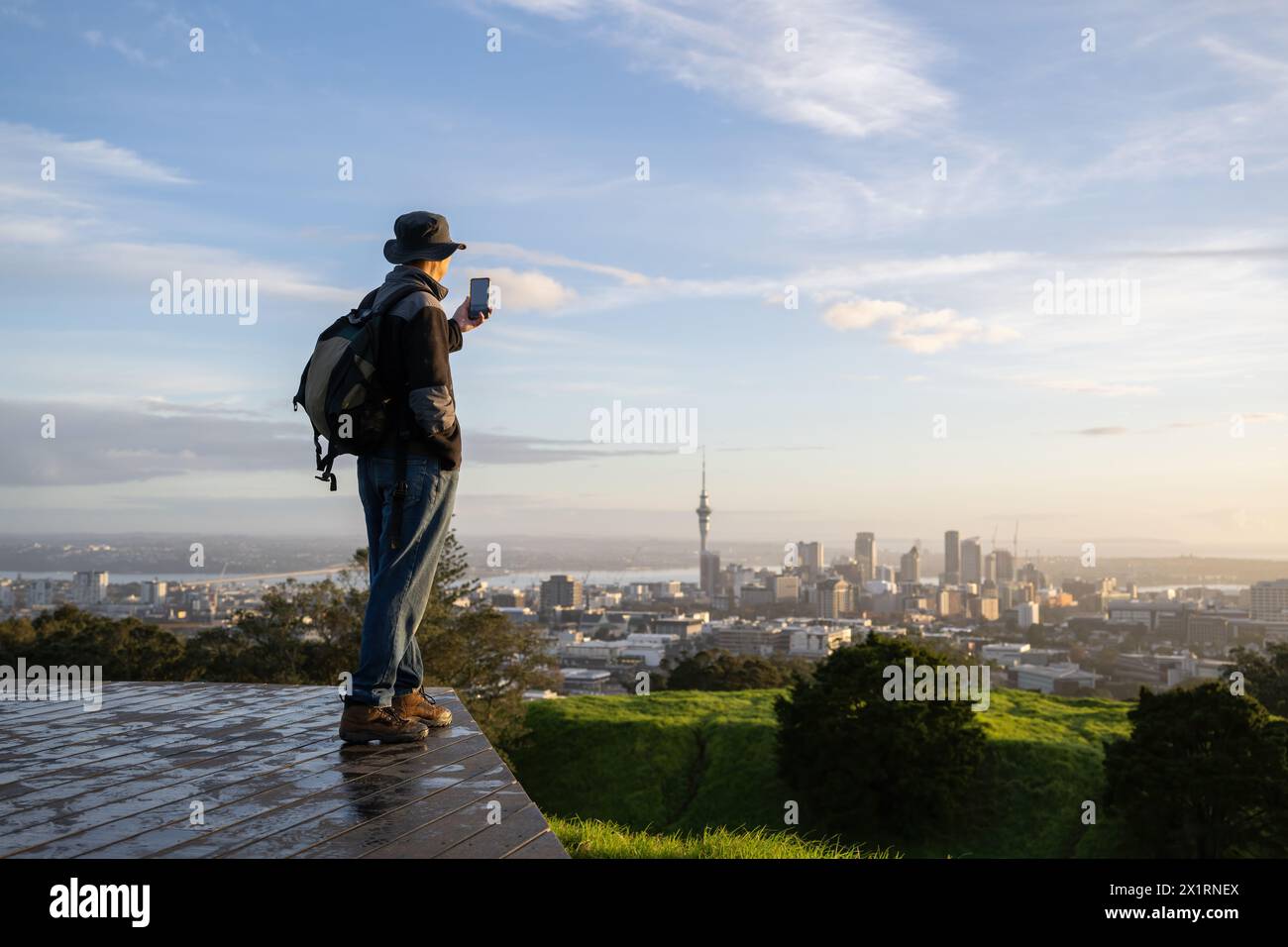 Tourist taking photos of Sky Tower and cityscape using smartphone. Mt ...