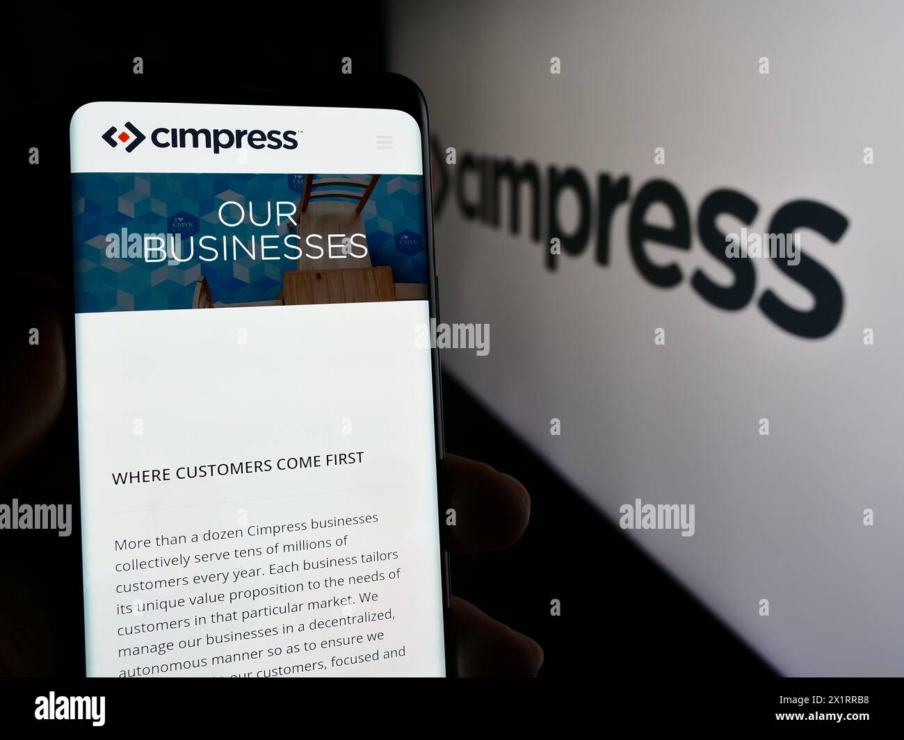 Person holding smartphone with web page of mass customization company Cimpress plc in front of ...