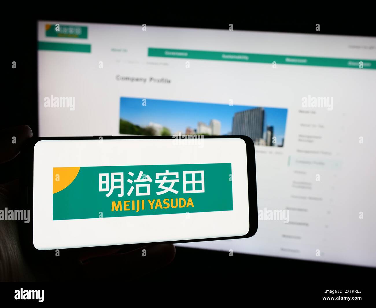 Person holding mobile phone with logo of Japanese business Meiji Yasuda ...