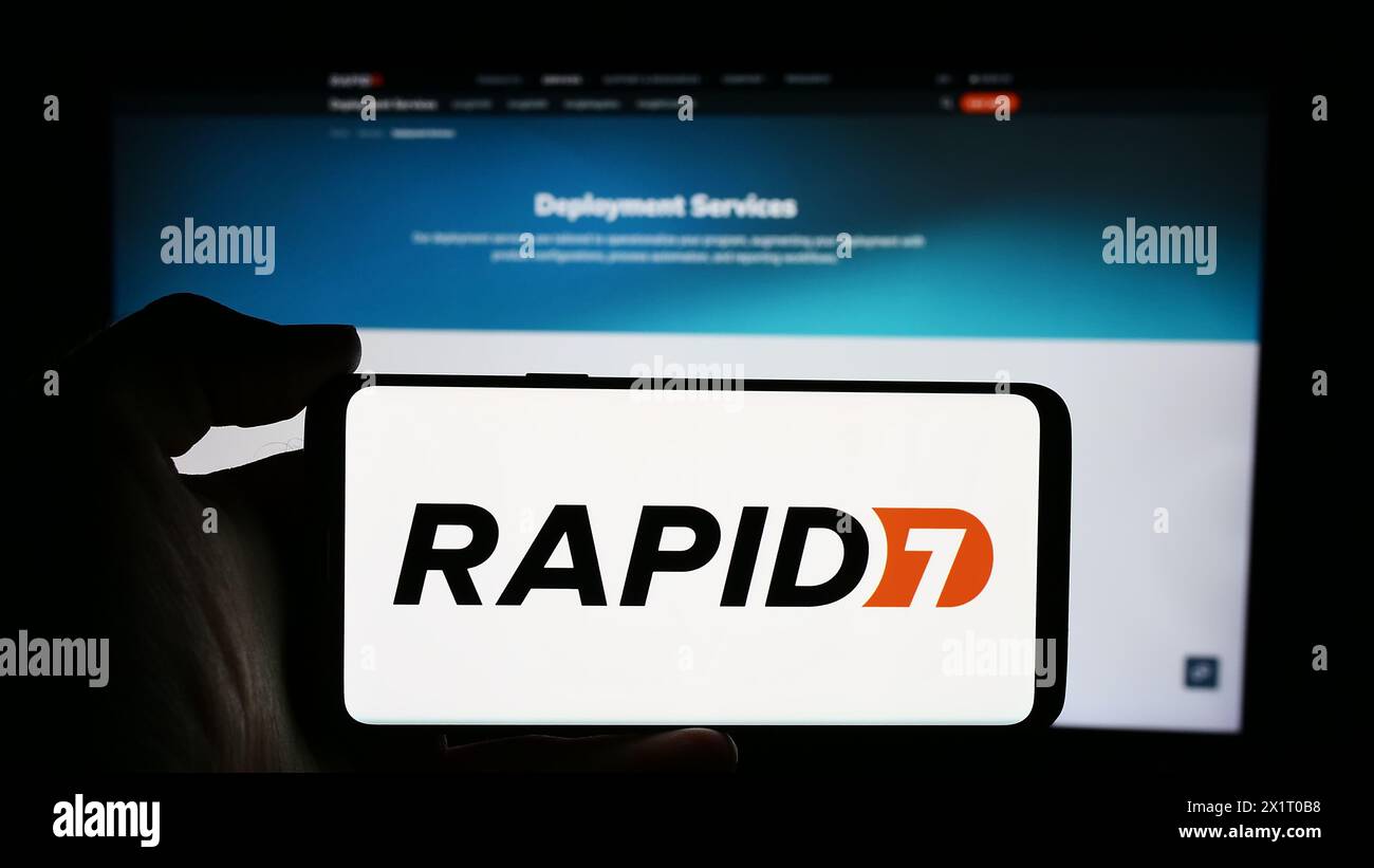Person holding cellphone with logo of US cyber security company Rapid7 ...