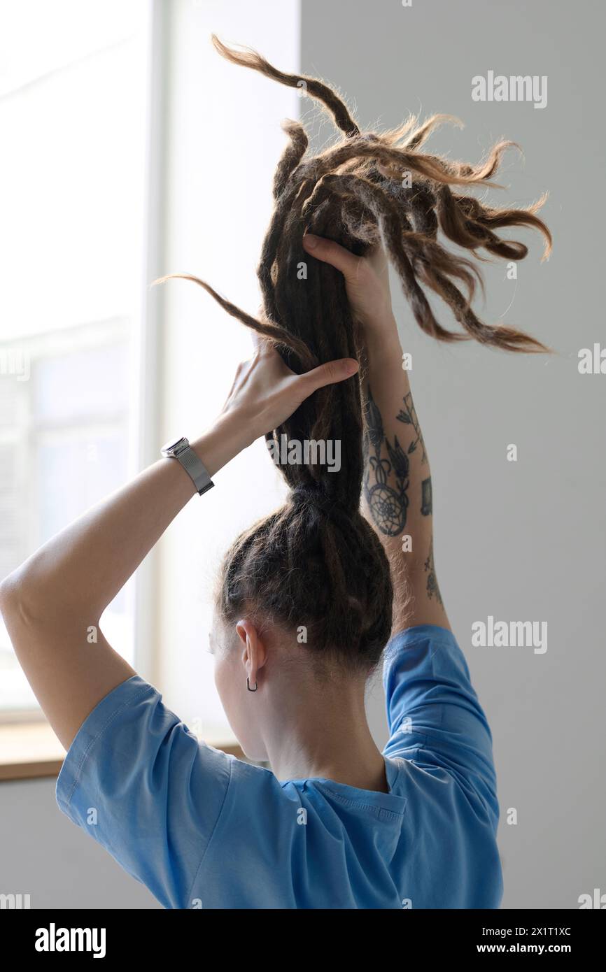 Vertical back view of young Caucasian woman holding long dreadlocks in ...