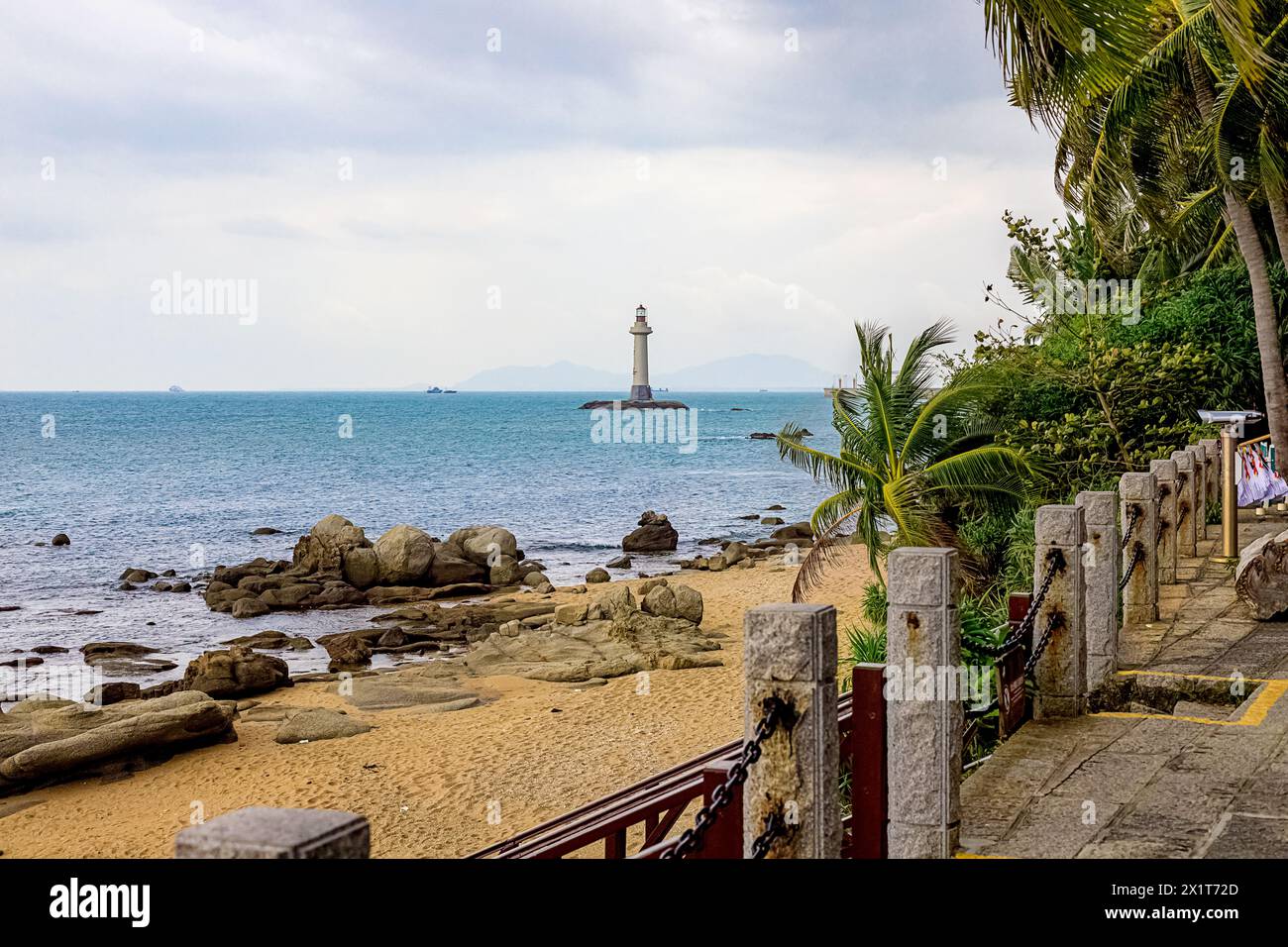 View of a lighthouse in the sea near a rocky shore with palm trees. End ...