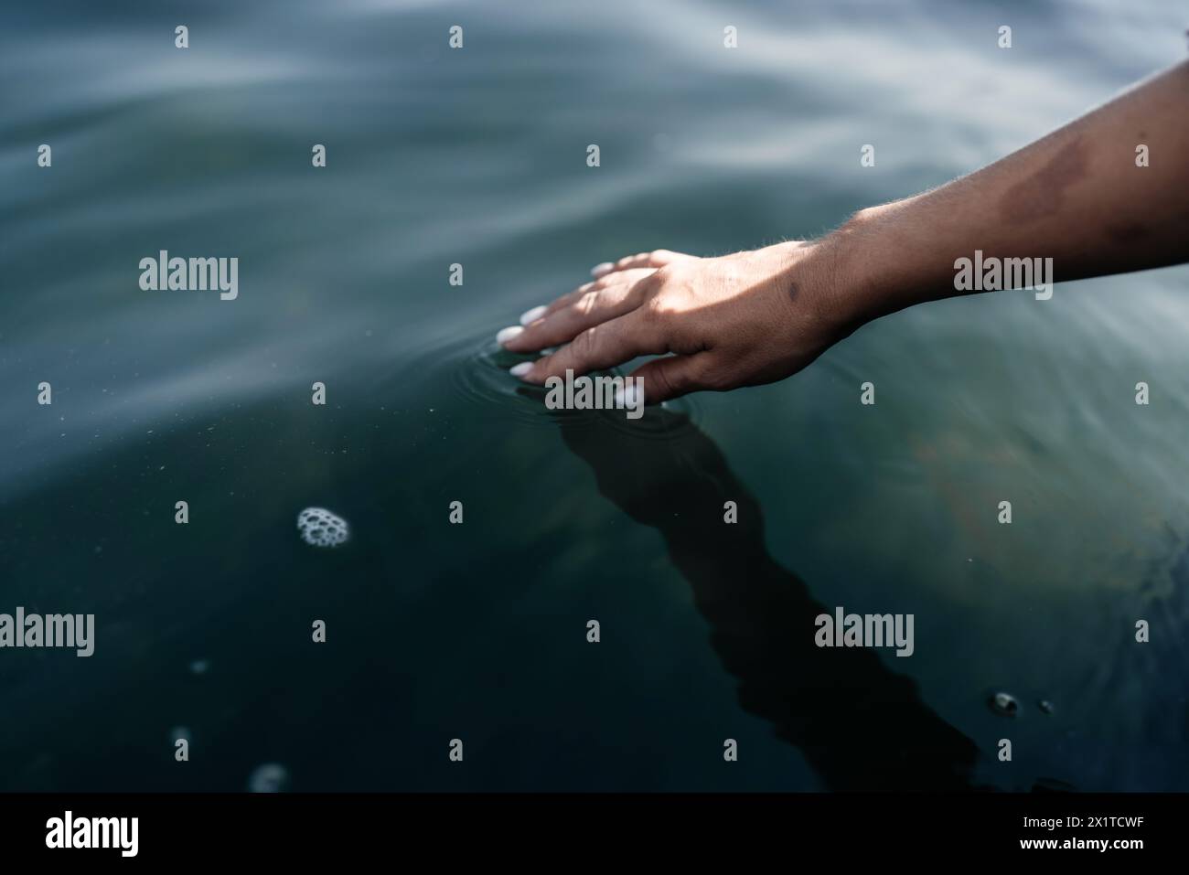 The hand touches the water, creating ripples. The water is calm and ...
