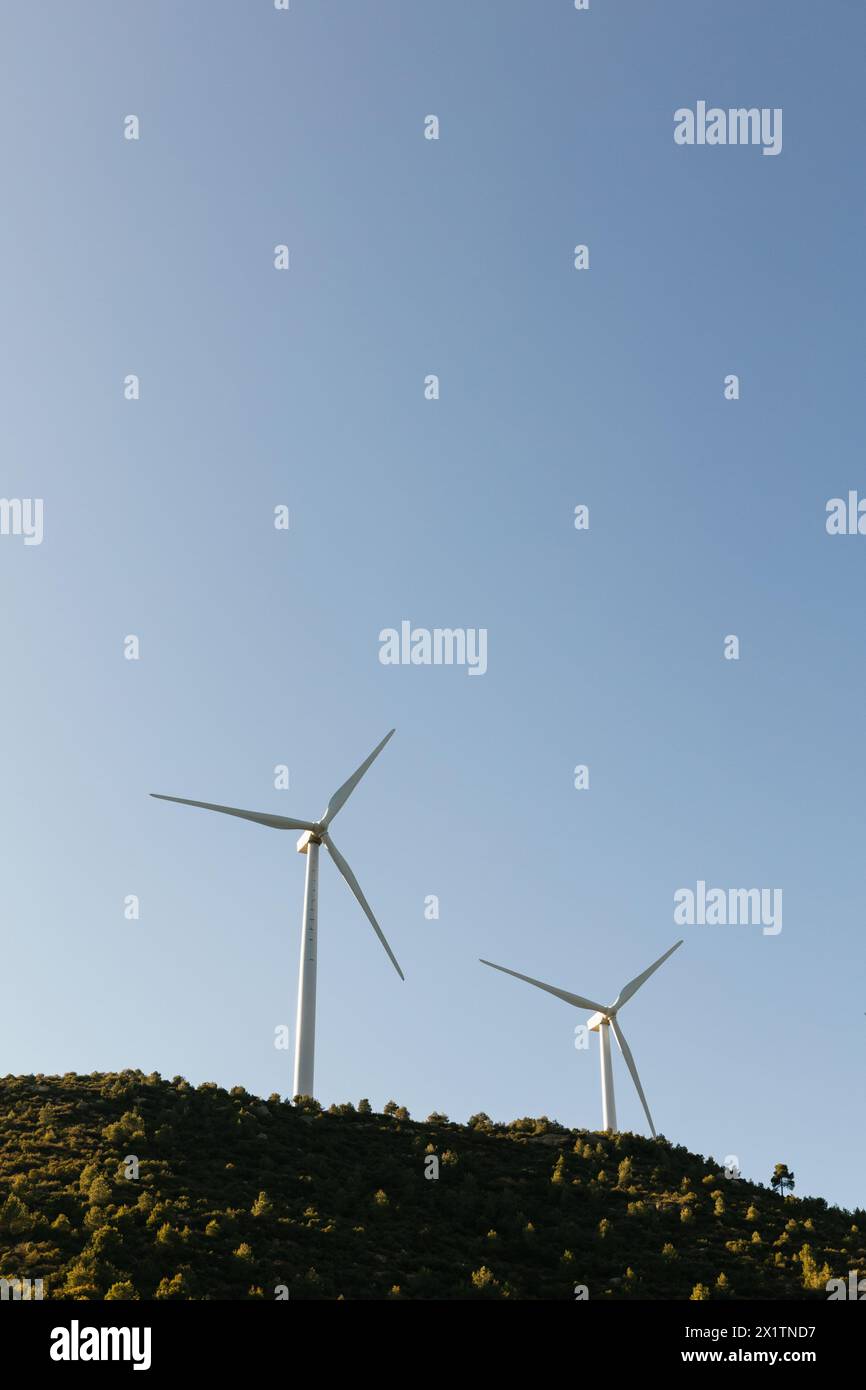 Two wind turbines spinning on a hilltop in a wind farm under a clear blue sky Stock Photo - Alamy