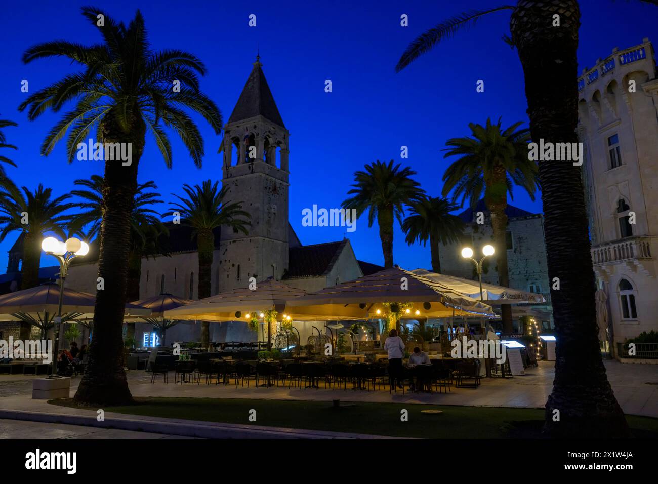 Outdoor restaurant at night with historic church tower and palm trees ...