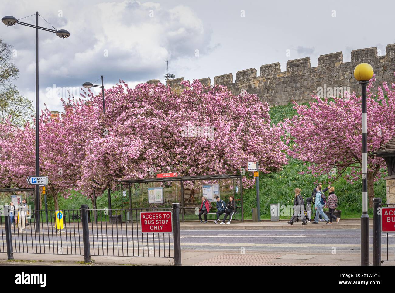 A bus stop underneath historic city walls. Seated passengers wait for a ...
