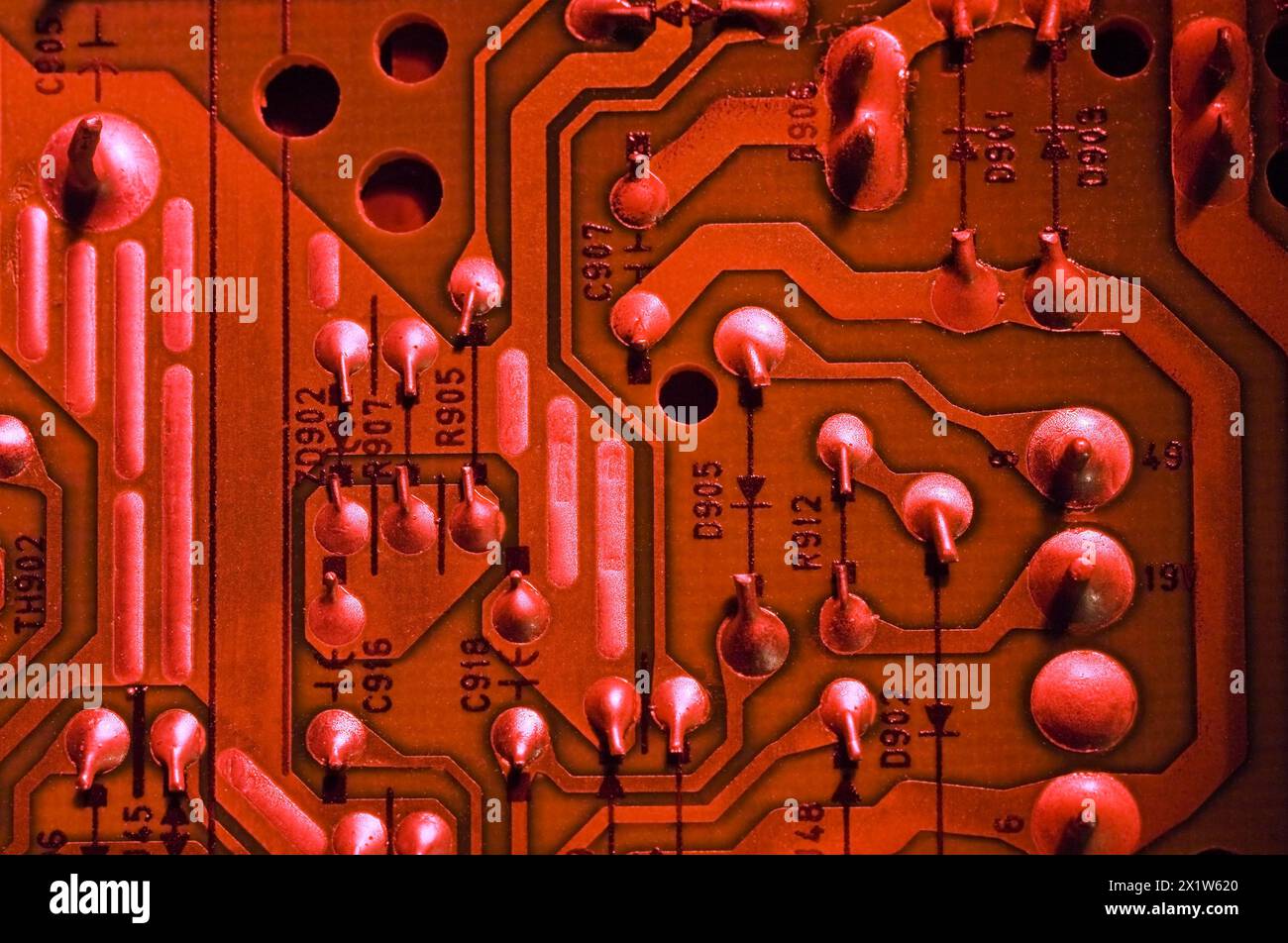 Close-up of red lighted electronic computer circuit board with silver solder points, numbers and ...