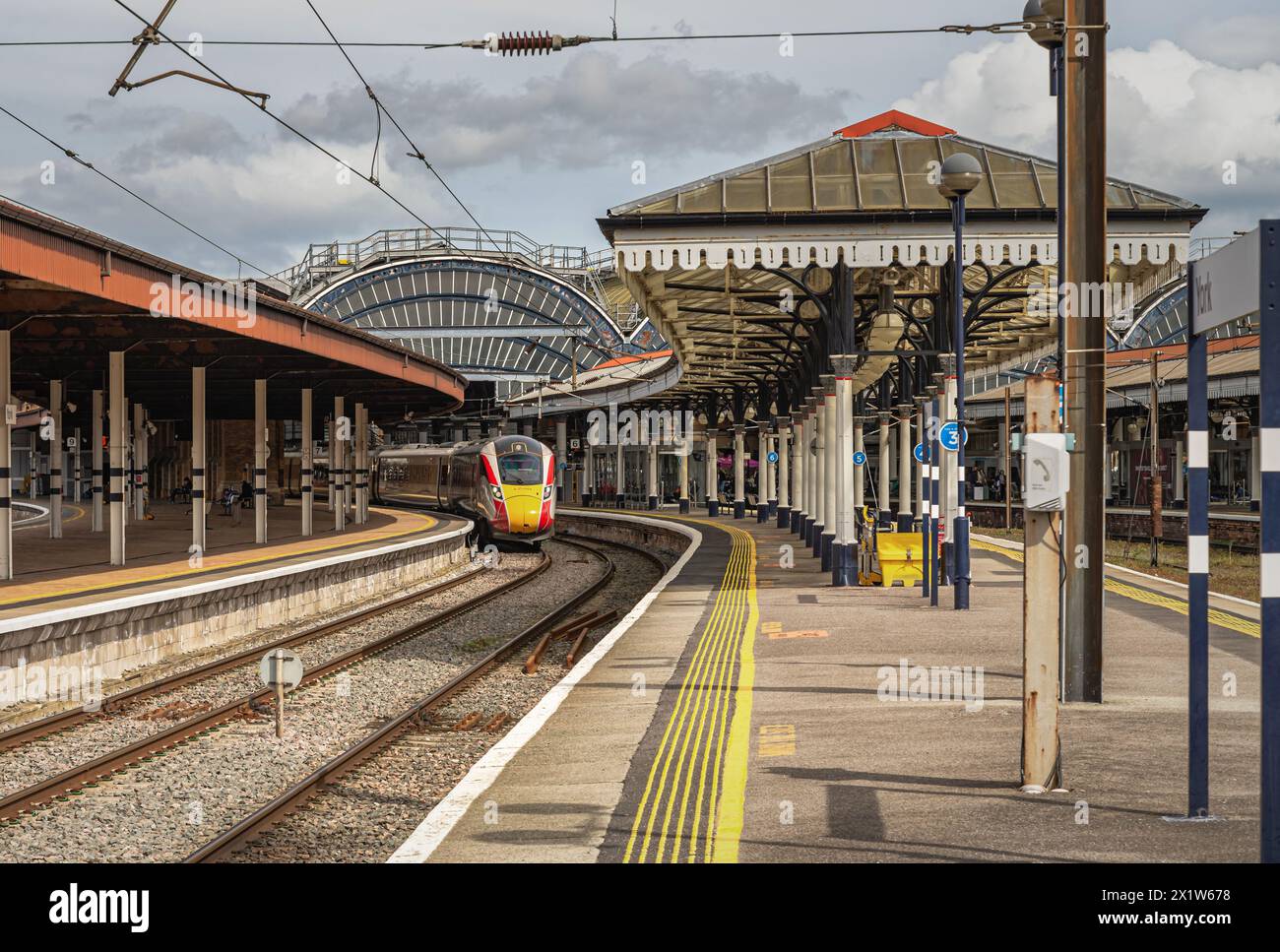 Departing train curves around a railway platform with a historic 19th Century canopy with ...
