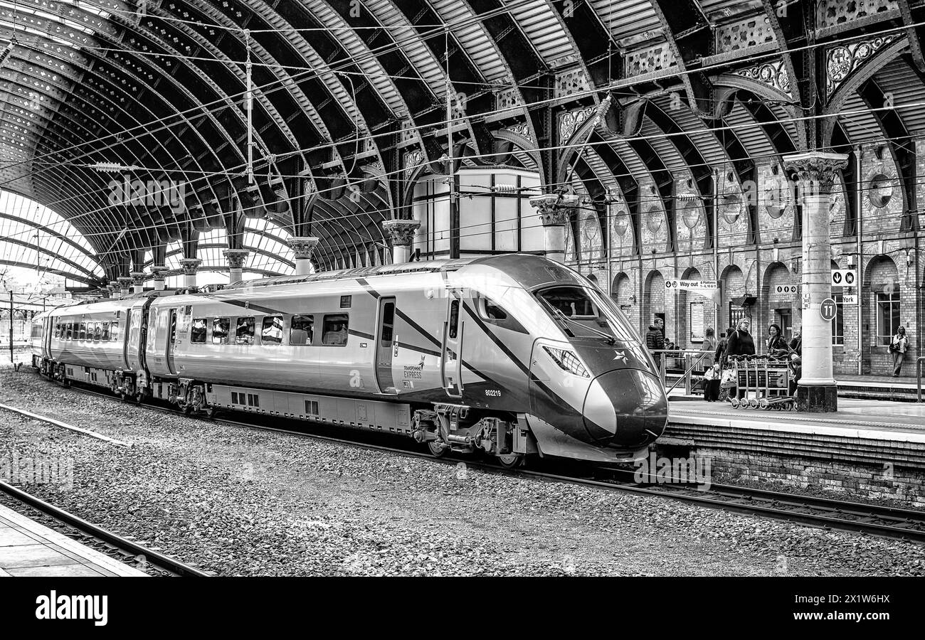 A modern train stands at a historic railway station platform under a ...