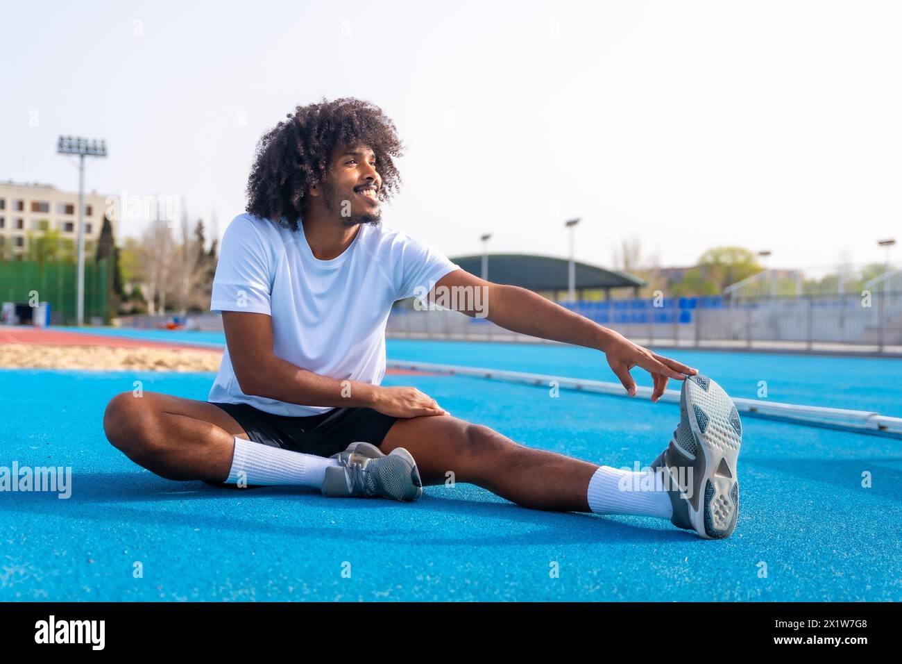 Side view of a smiling young african sportive man stretching sitting on ...