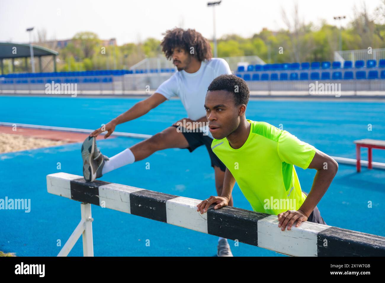 Two young african american runners stretching legs in a fence in a ...