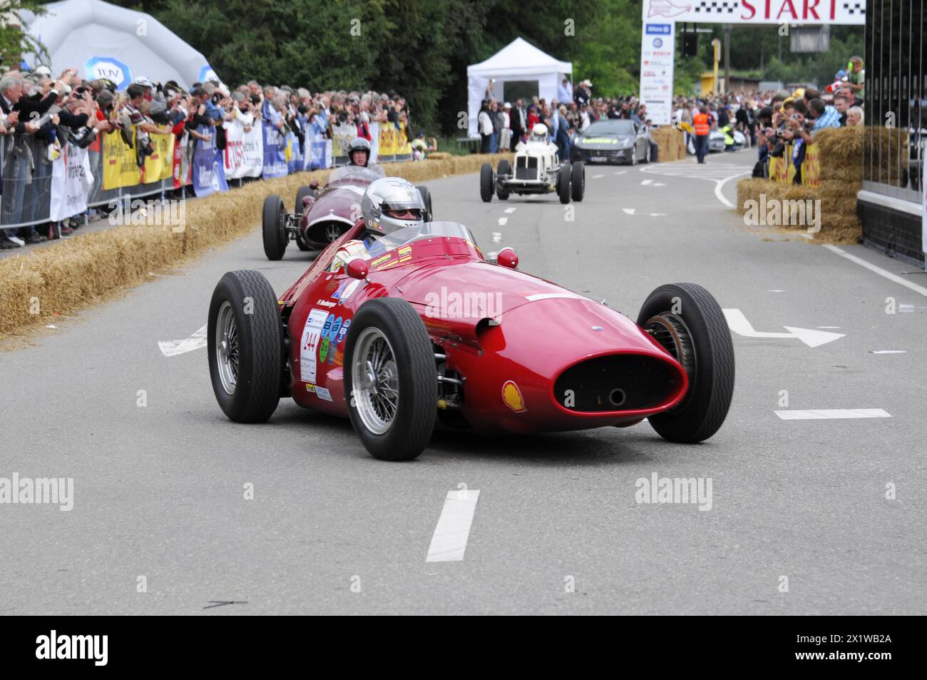 A red classic formula racing car drives past spectators on a cordoned ...