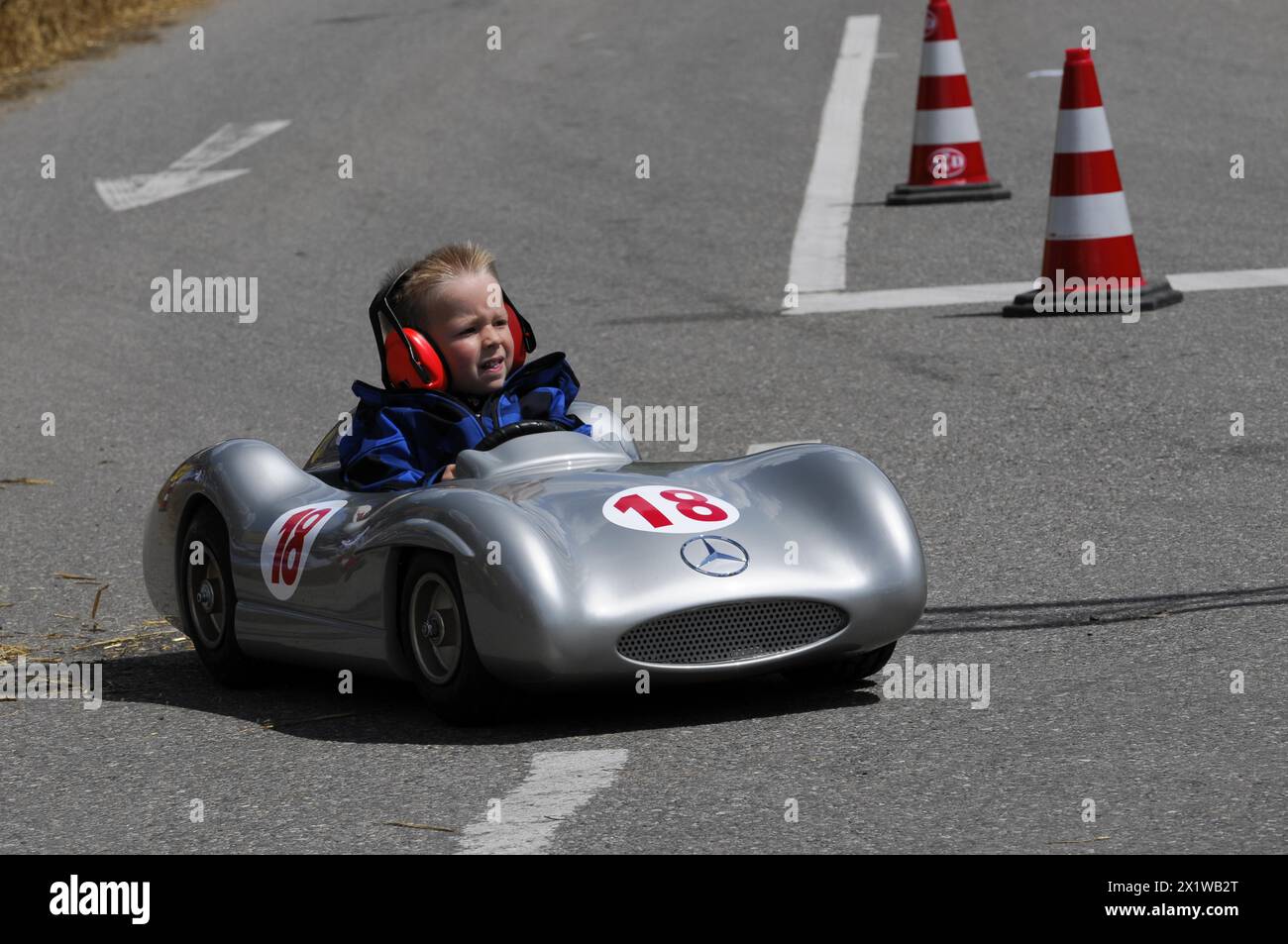 A child in a silver soapbox racing car with the number 18 drives past ...