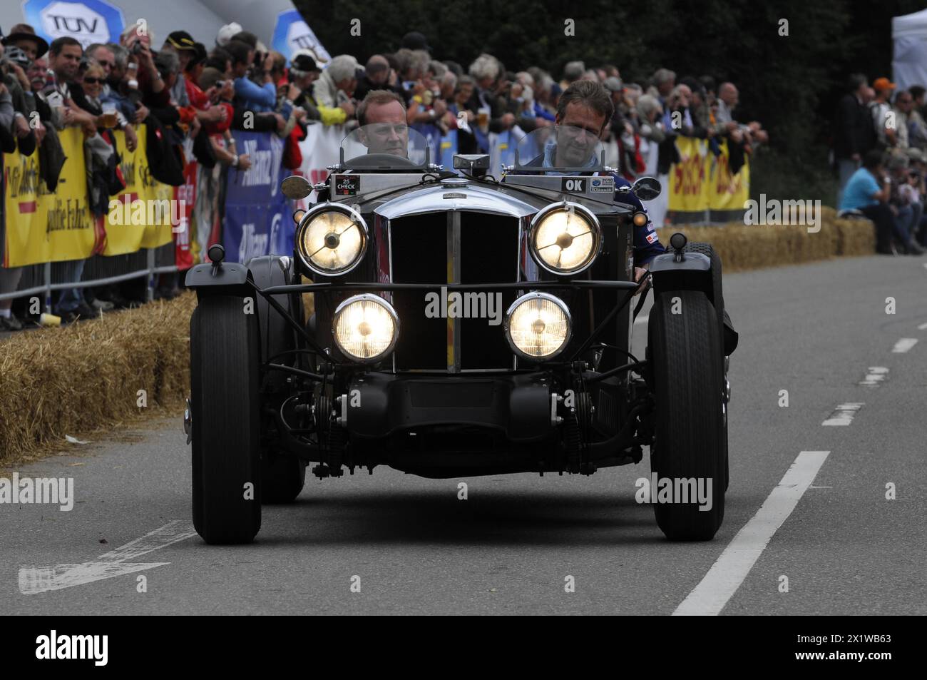 Historic racing car drives past the public at night with its headlights ...