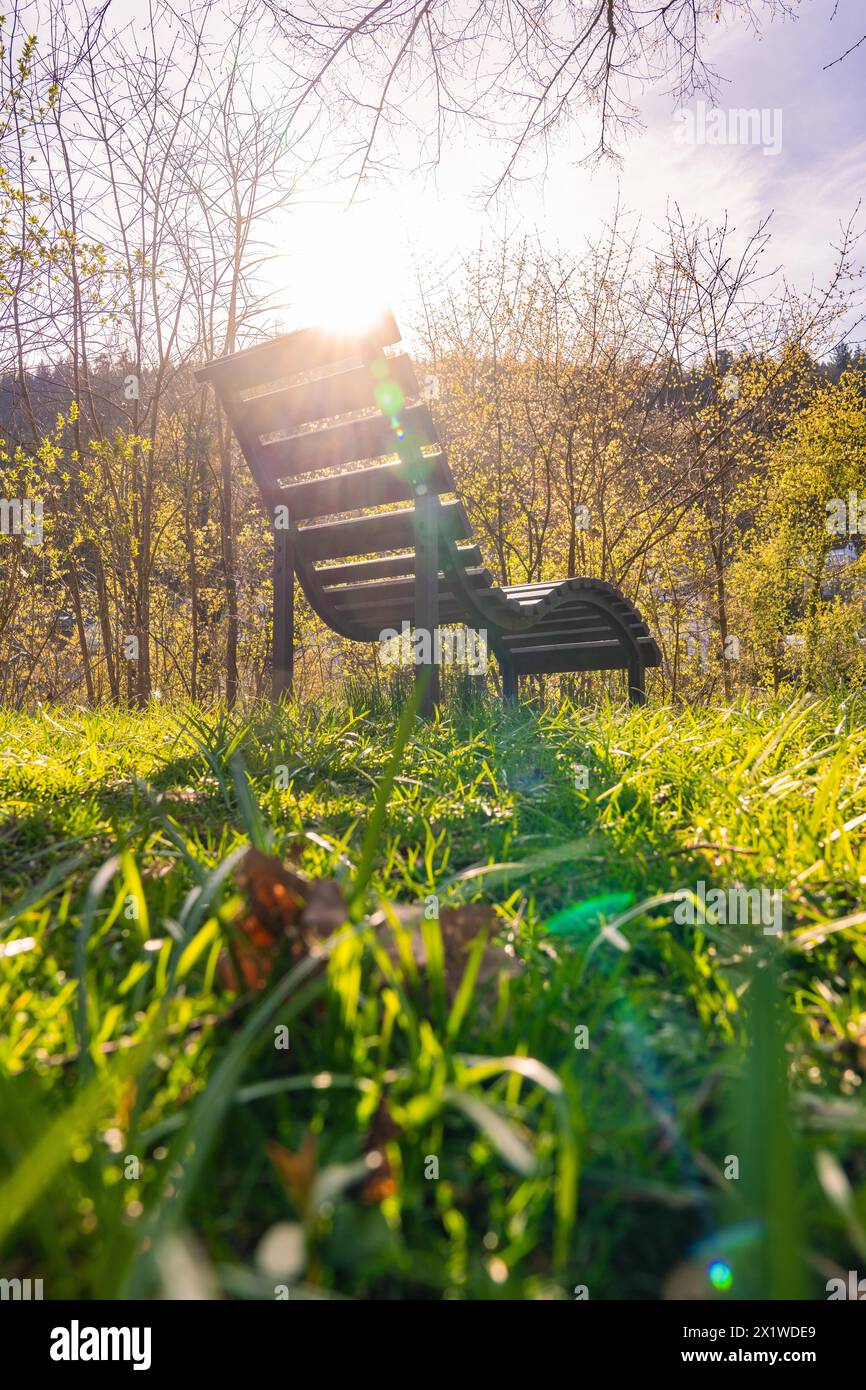An empty park bench in the grass illuminated by early morning sunbeams ...