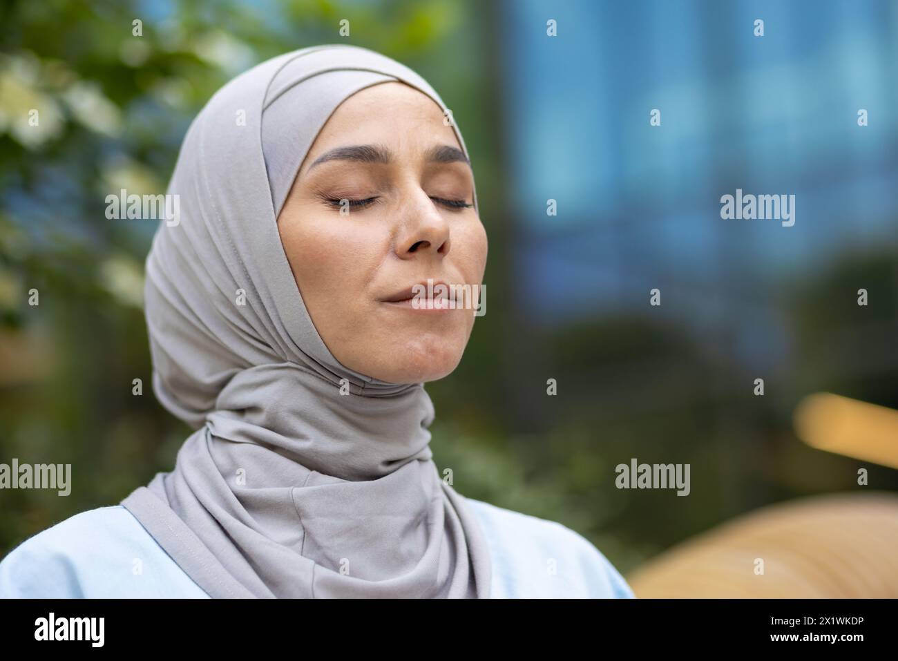 A serene portrait of a Muslim woman meditating with closed eyes, wearing a hijab, in a verdant ...