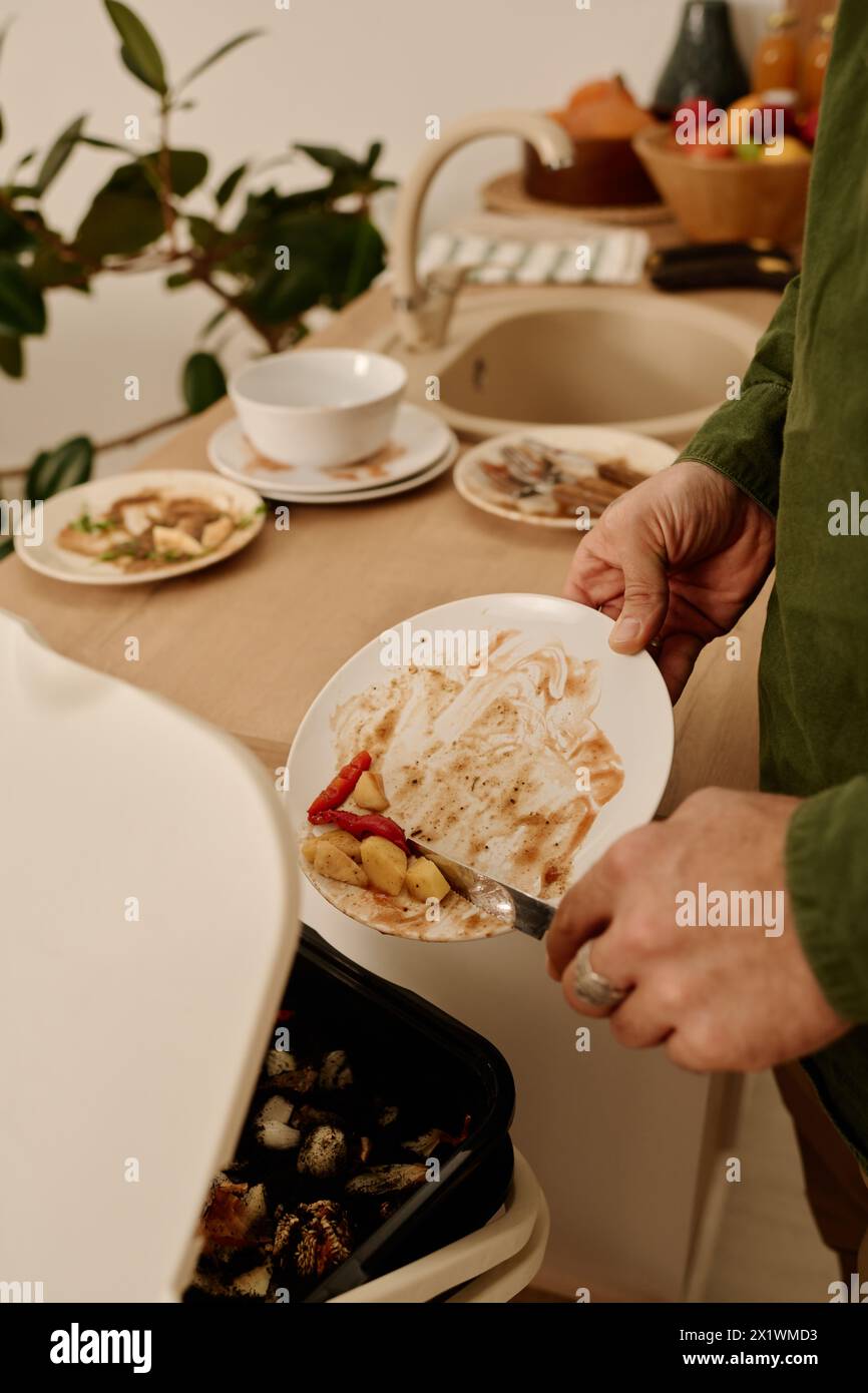 Hands of young man putting organic leftovers in trash bin with soil ...