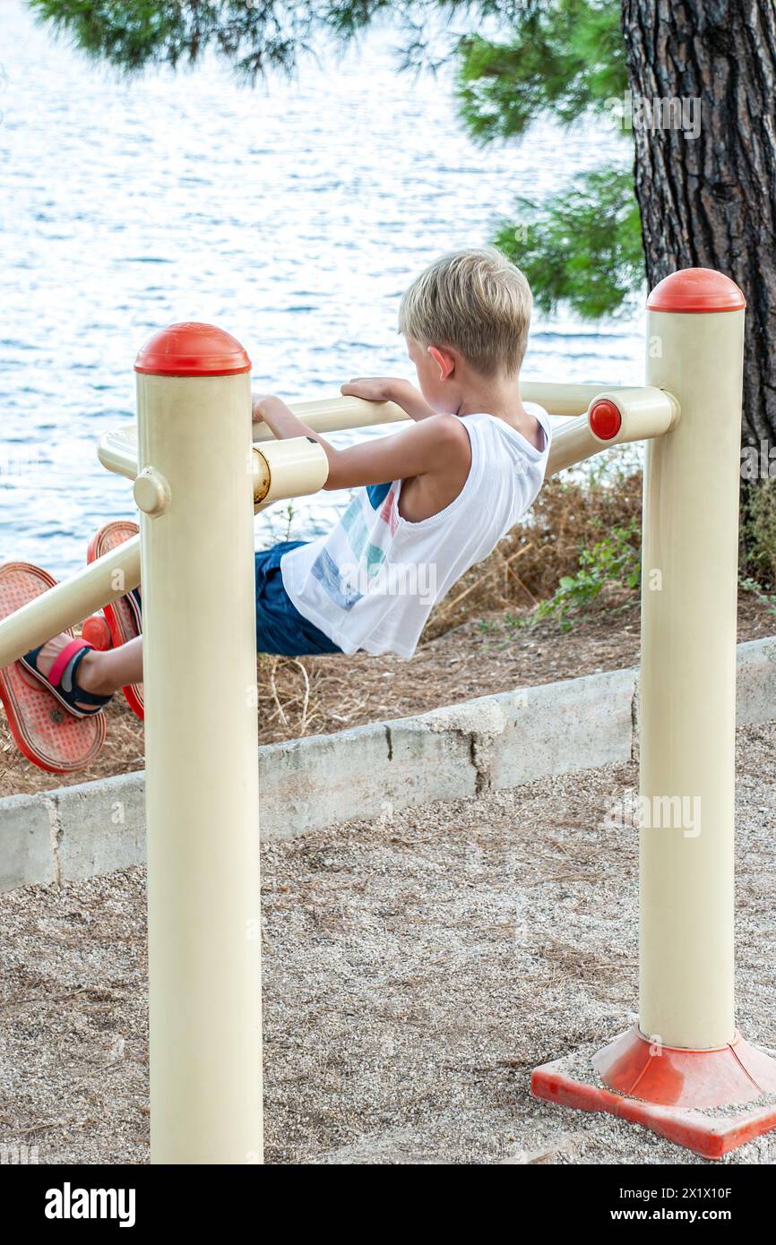 Young boy engaging in physical exercise on an outdoor gym apparatus ...