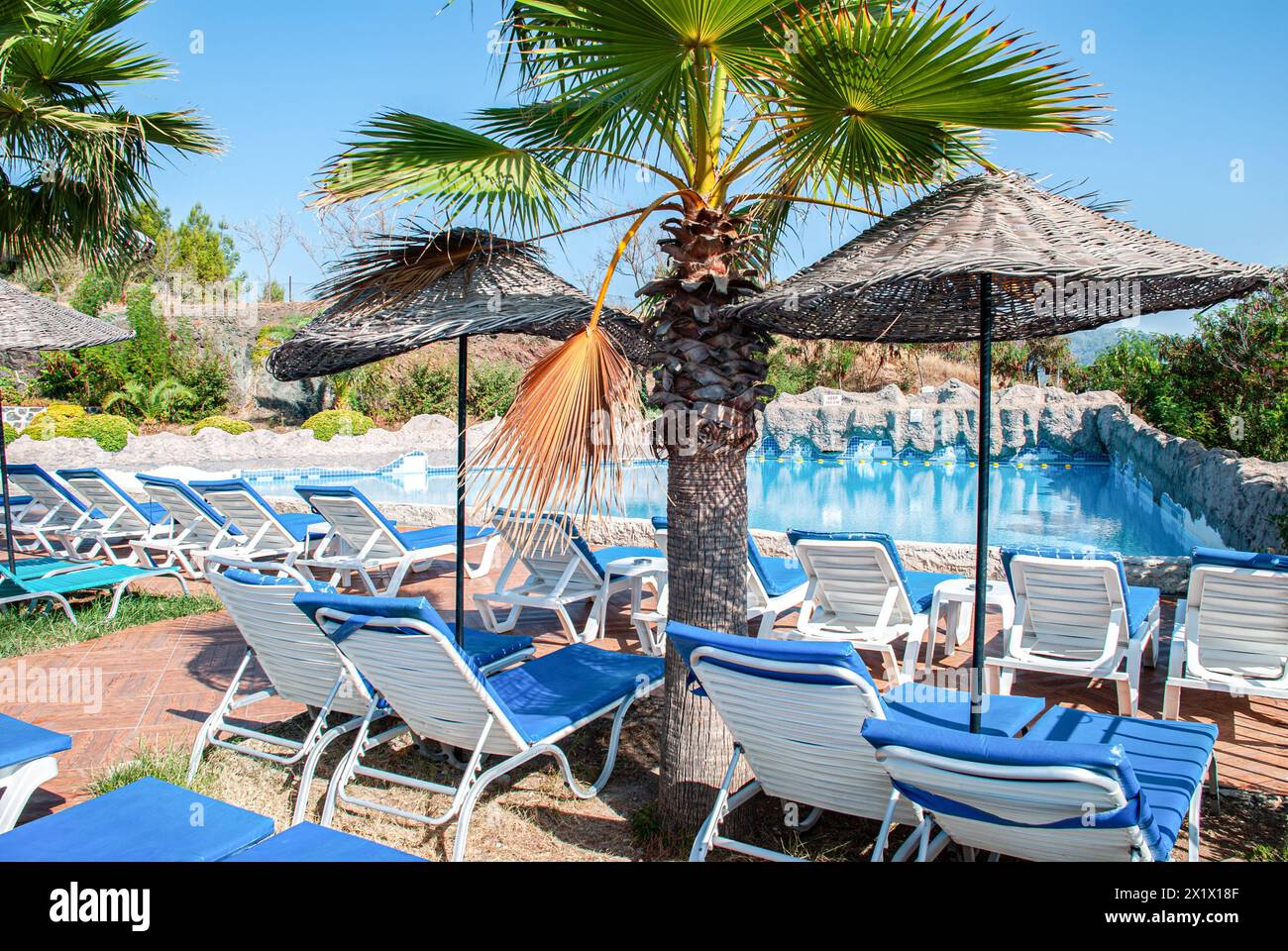 Outdoor swimming pool area in a water park with sun loungers and straw ...