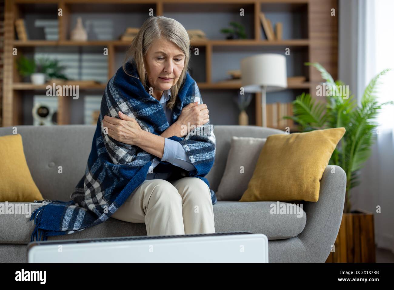 Sick senior lady hugging herself while sitting covered with checkered ...