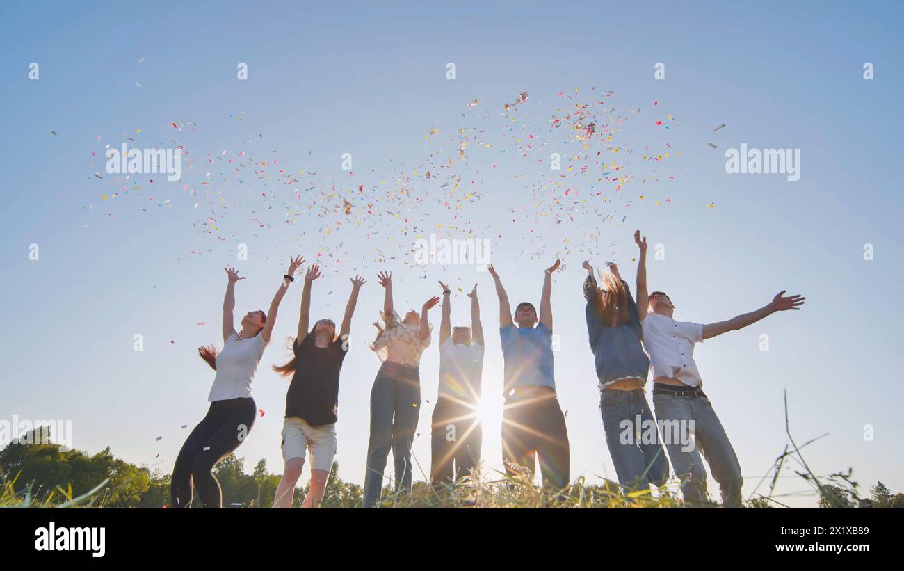 Friends toss colorful paper confetti from their hands against the rays ...