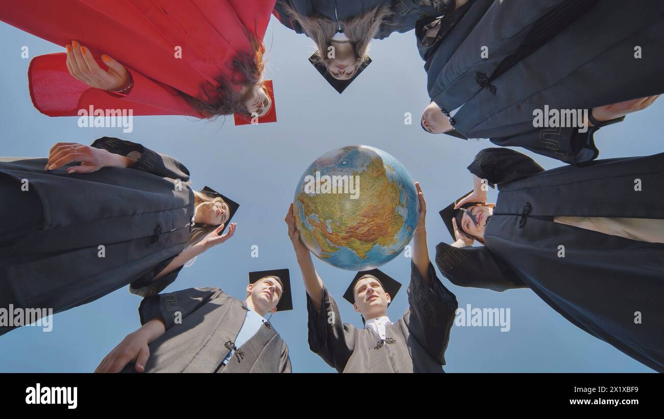 College graduates stand in a circle and hold a geographical globe of ...