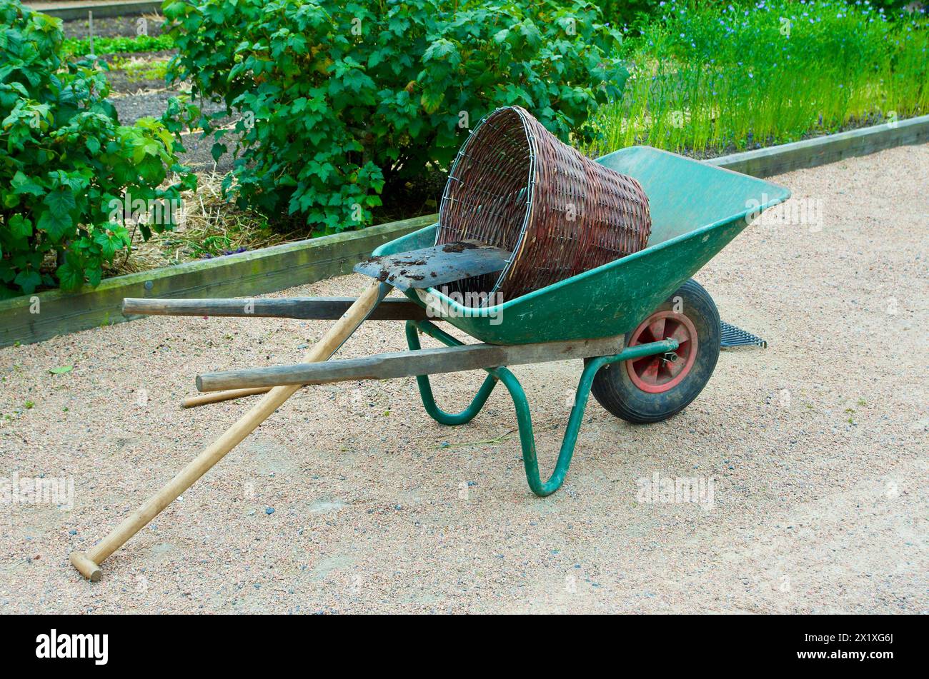Green common wheelbarrow loaded with a garden spade and a plaited ...