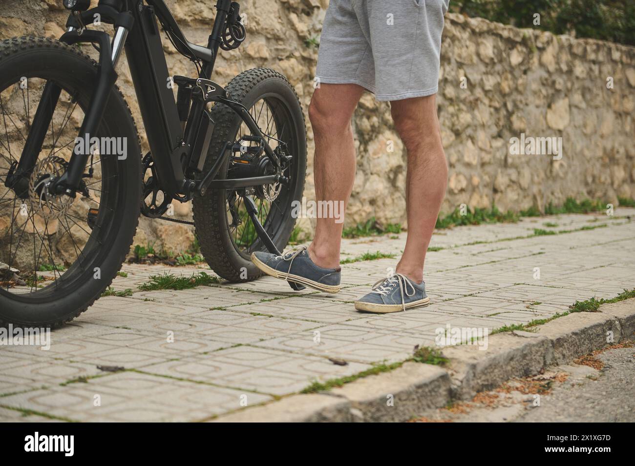 Close-up legs of a cyclist in sports shoes, pushing his bike while ...