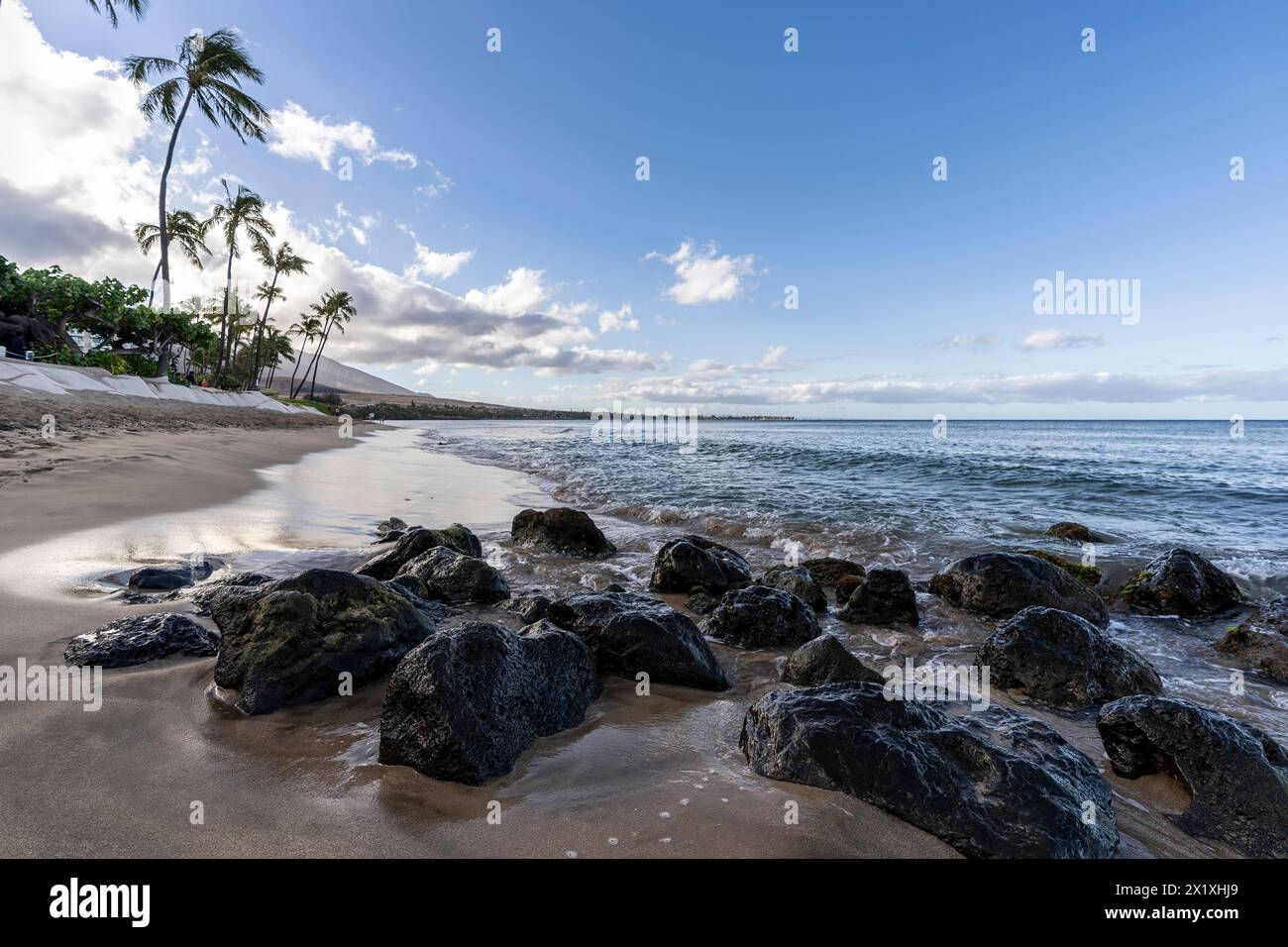 Waves crash over large volcanic rocks embedded in the sand along the ...