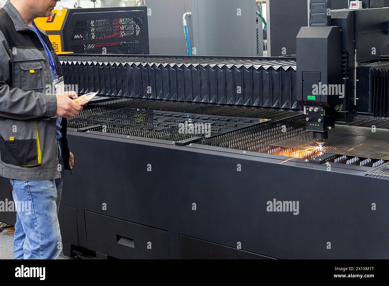 A worker operates a steel laser cutting machine at a factory. Industry ...