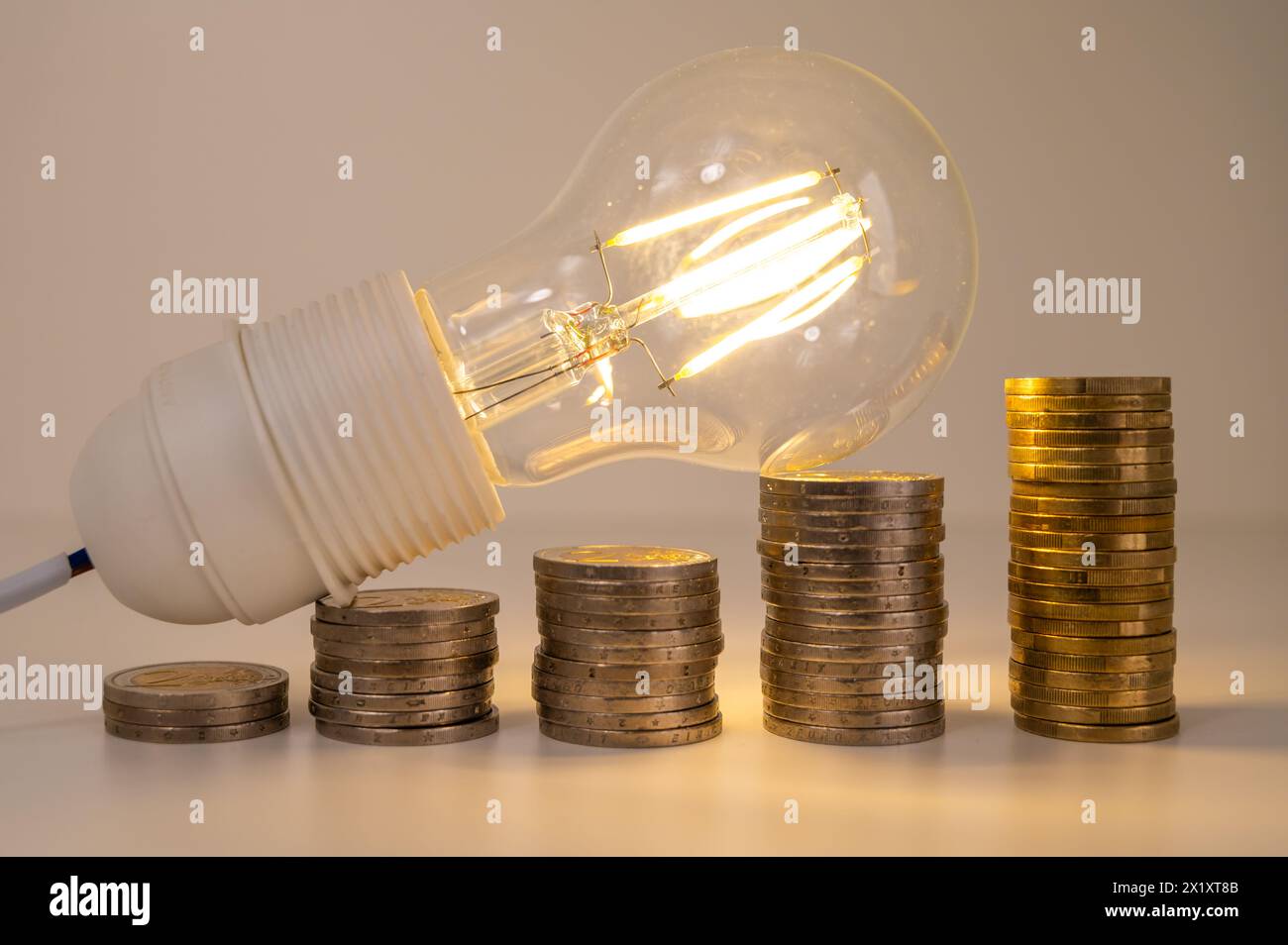 Light bulb lit, above stacks of coins. Increase in electricity tariffs ...