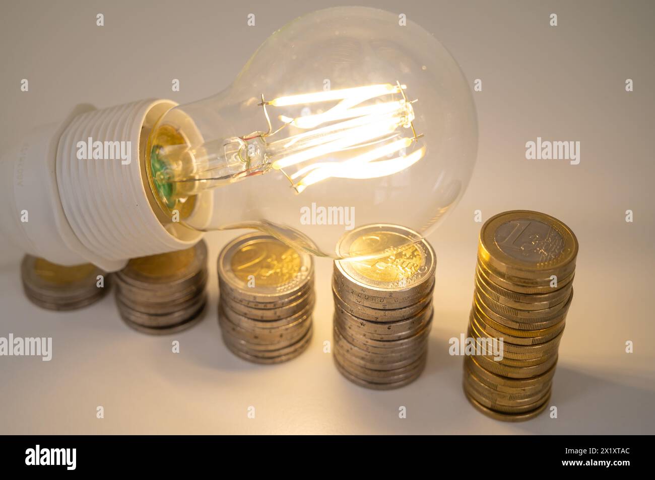 Light bulb lit, above stacks of coins. Increase in electricity tariffs ...