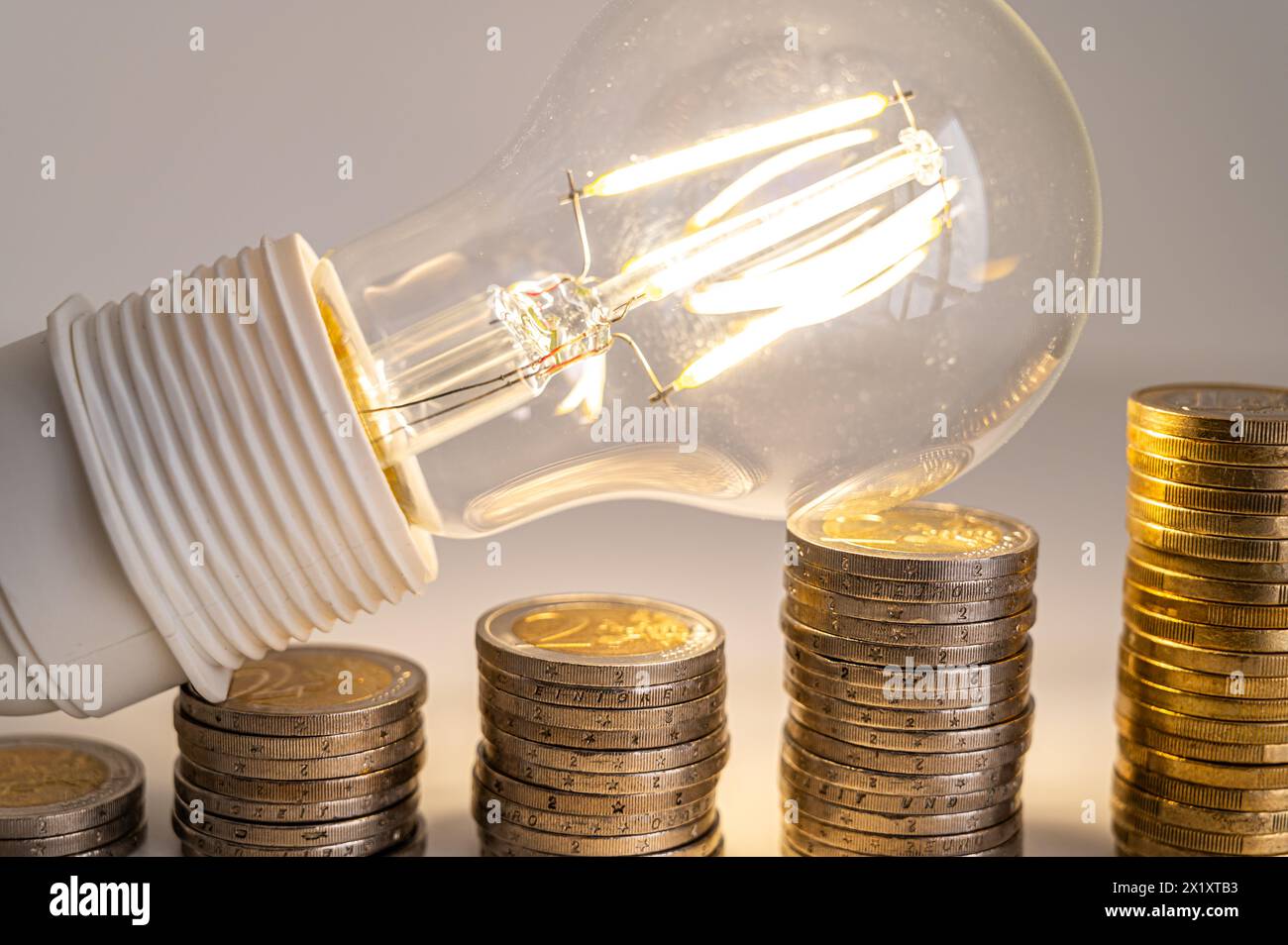 Light bulb lit, above stacks of coins. Increase in electricity tariffs ...