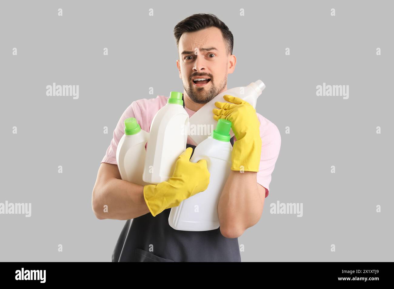Stressed male janitor with bottles of detergent on grey background ...